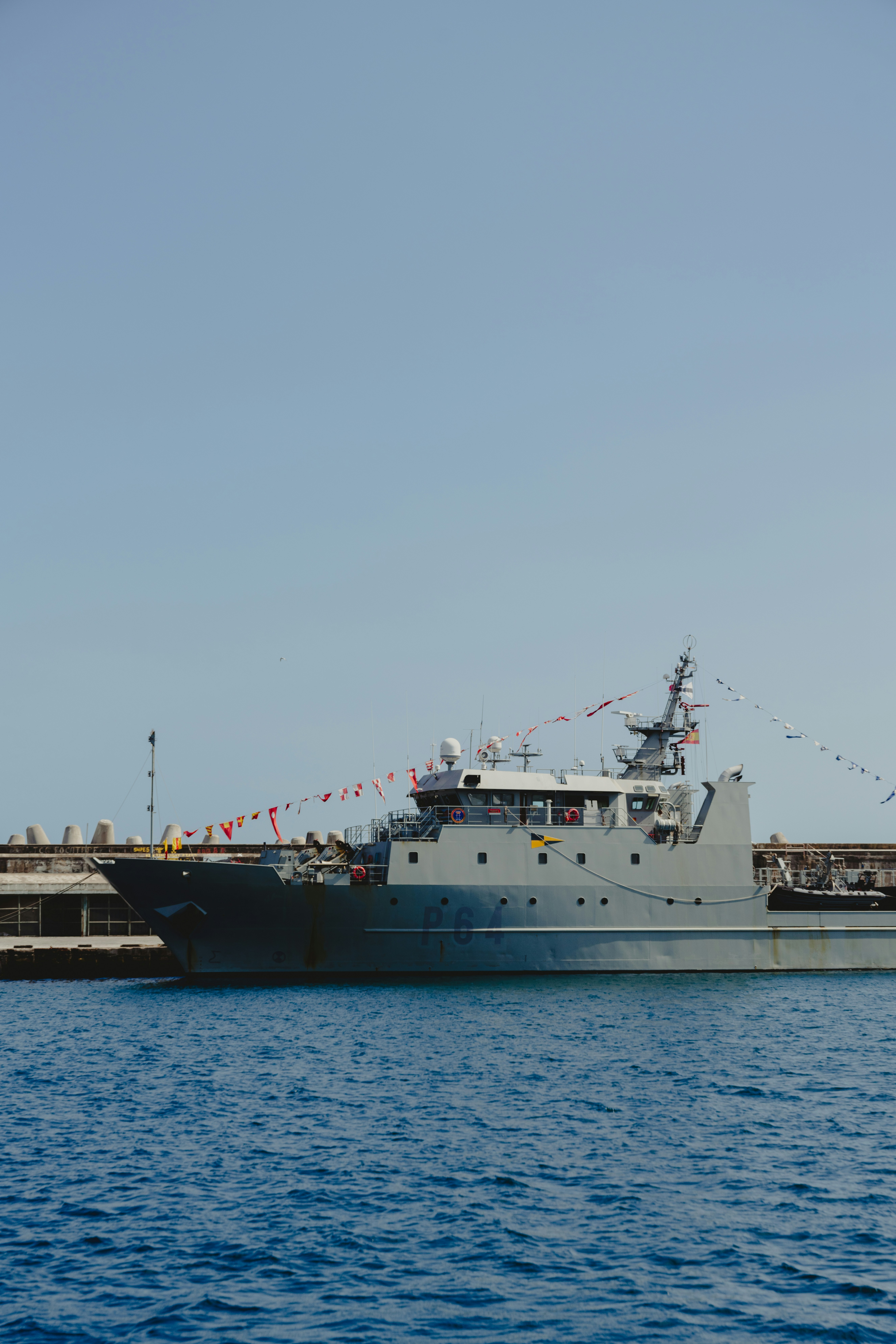 Dockside Guardian: A gray naval vessel strung with ceremonial pennants against a calm blue backdrop