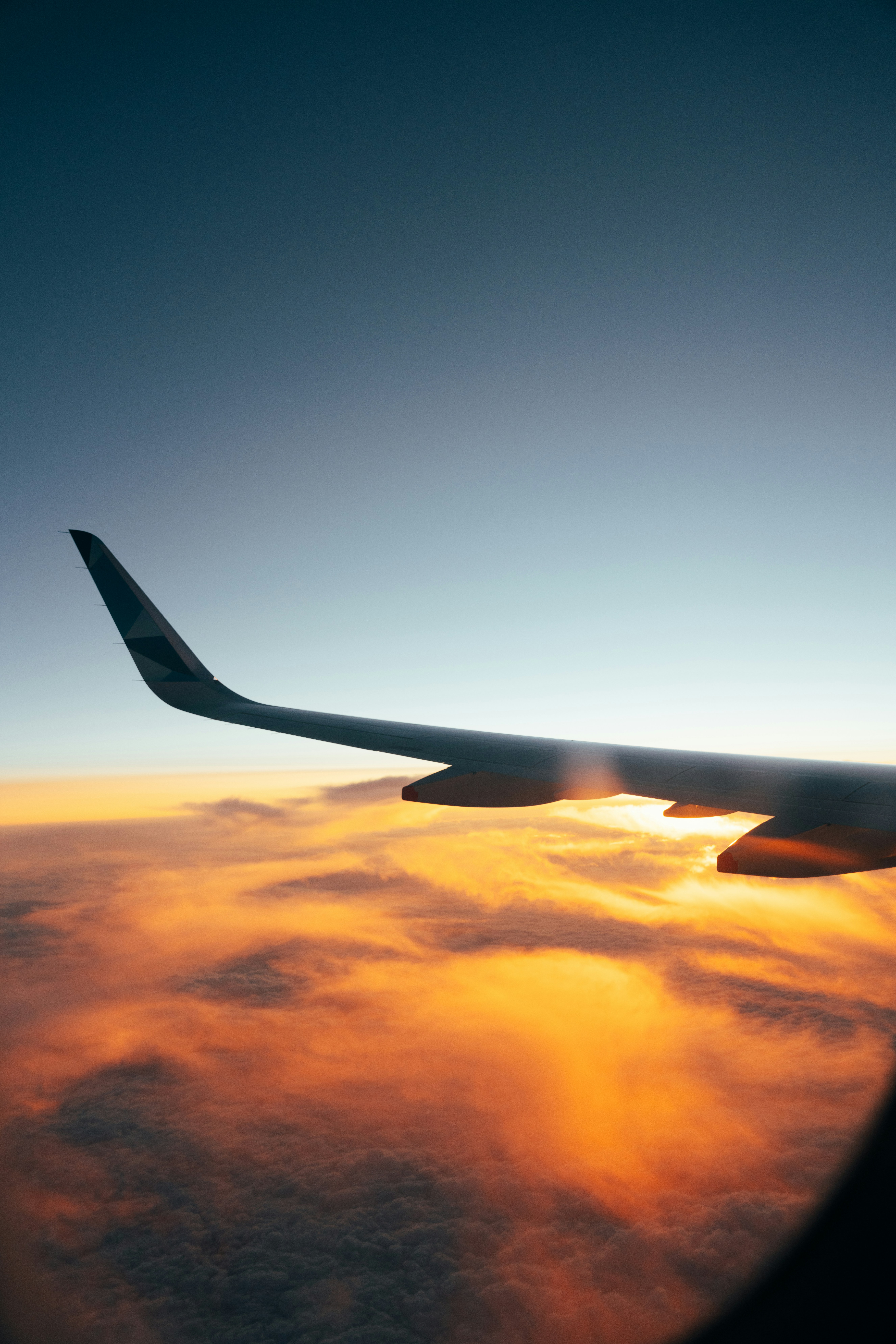 Airplane wing silhouetted against a vibrant sunset, casting warm hues over the clouds. A serene moment captured during flight.
