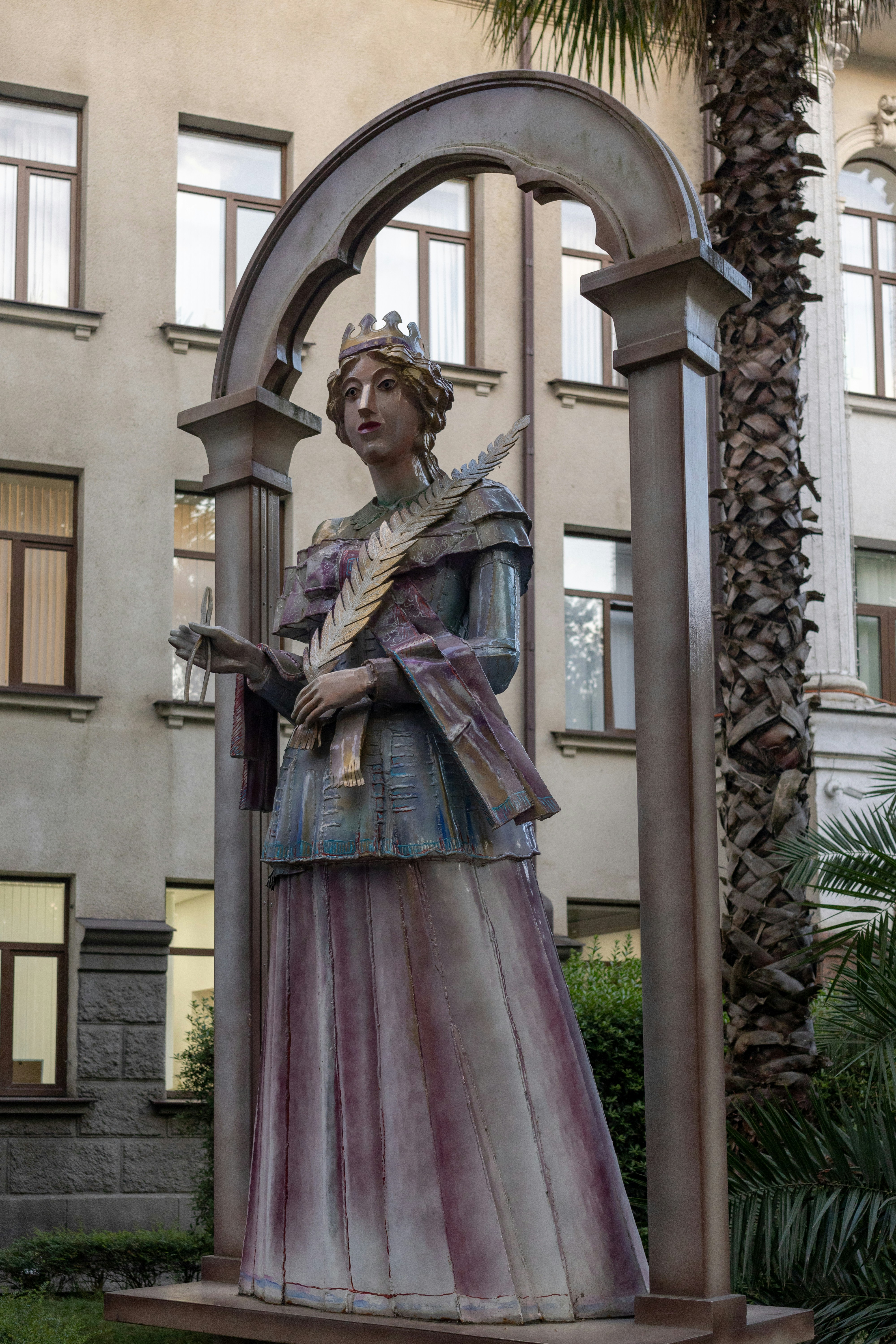 Feathered Queen Under the Arch: a weathered urban sculpture amid palms