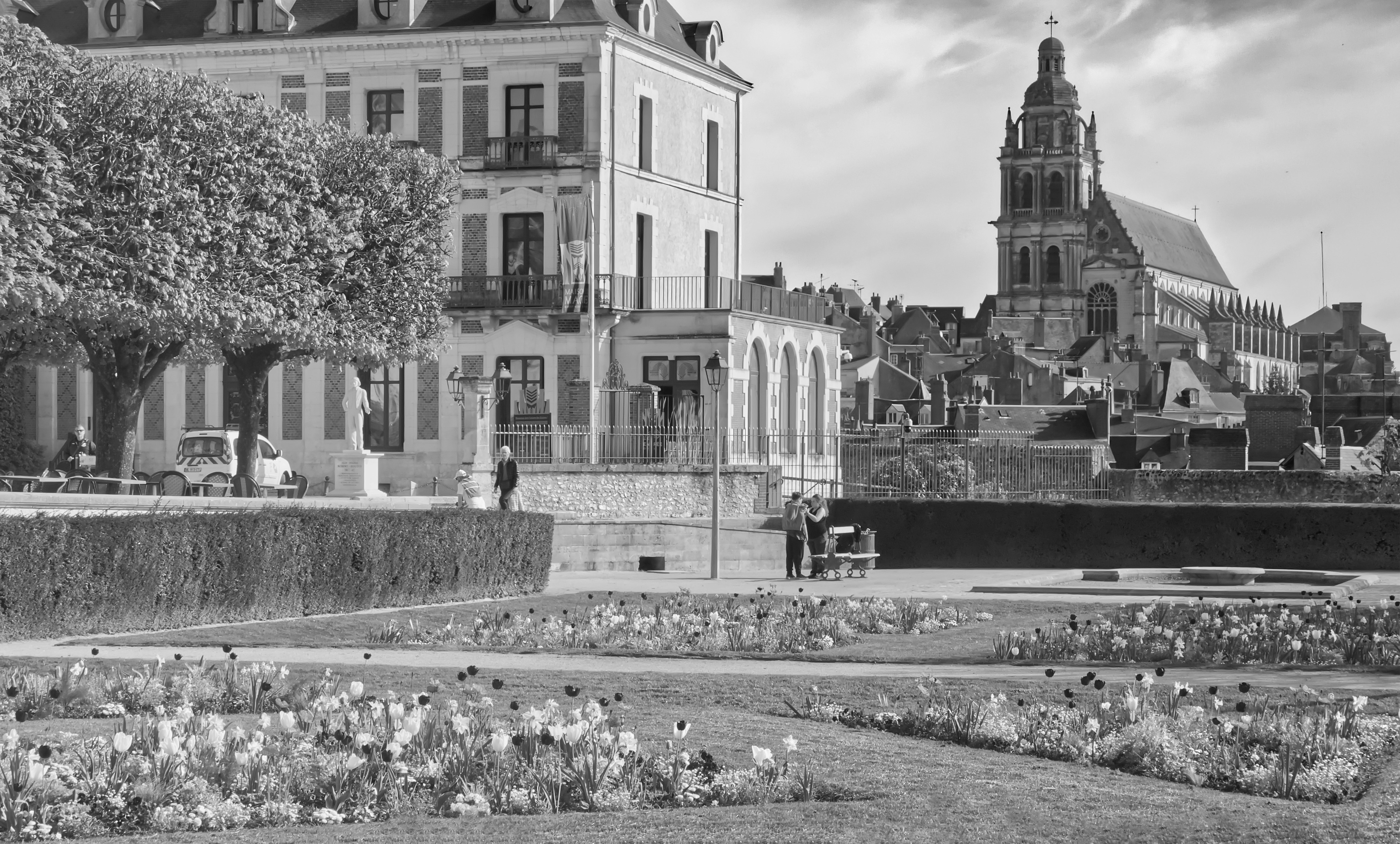 Black and white view of a grand building with a cathedral in the background, framed by gardens.