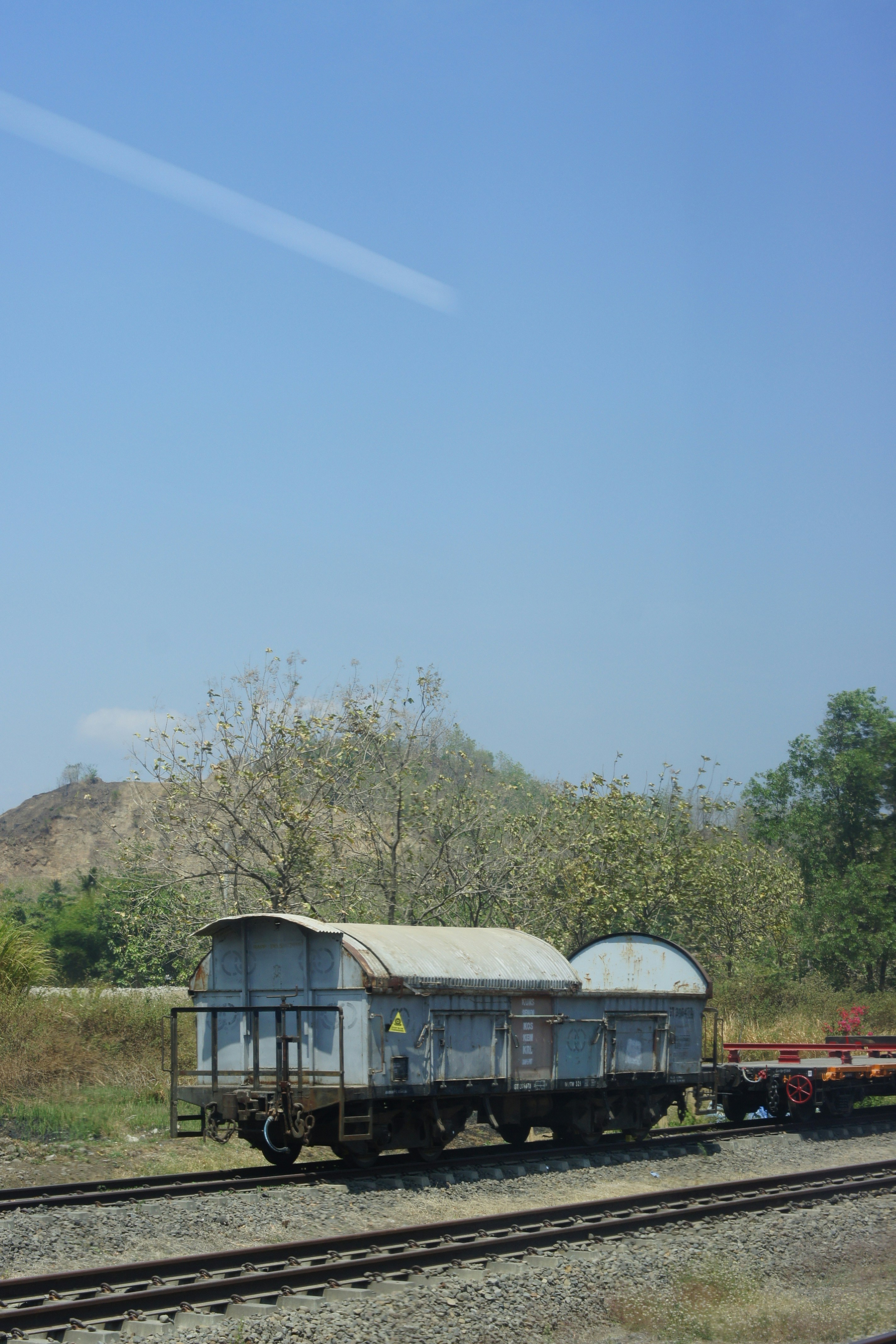 Abandoned train car resting on railroad tracks, surrounded by sparse vegetation under a clear blue sky.