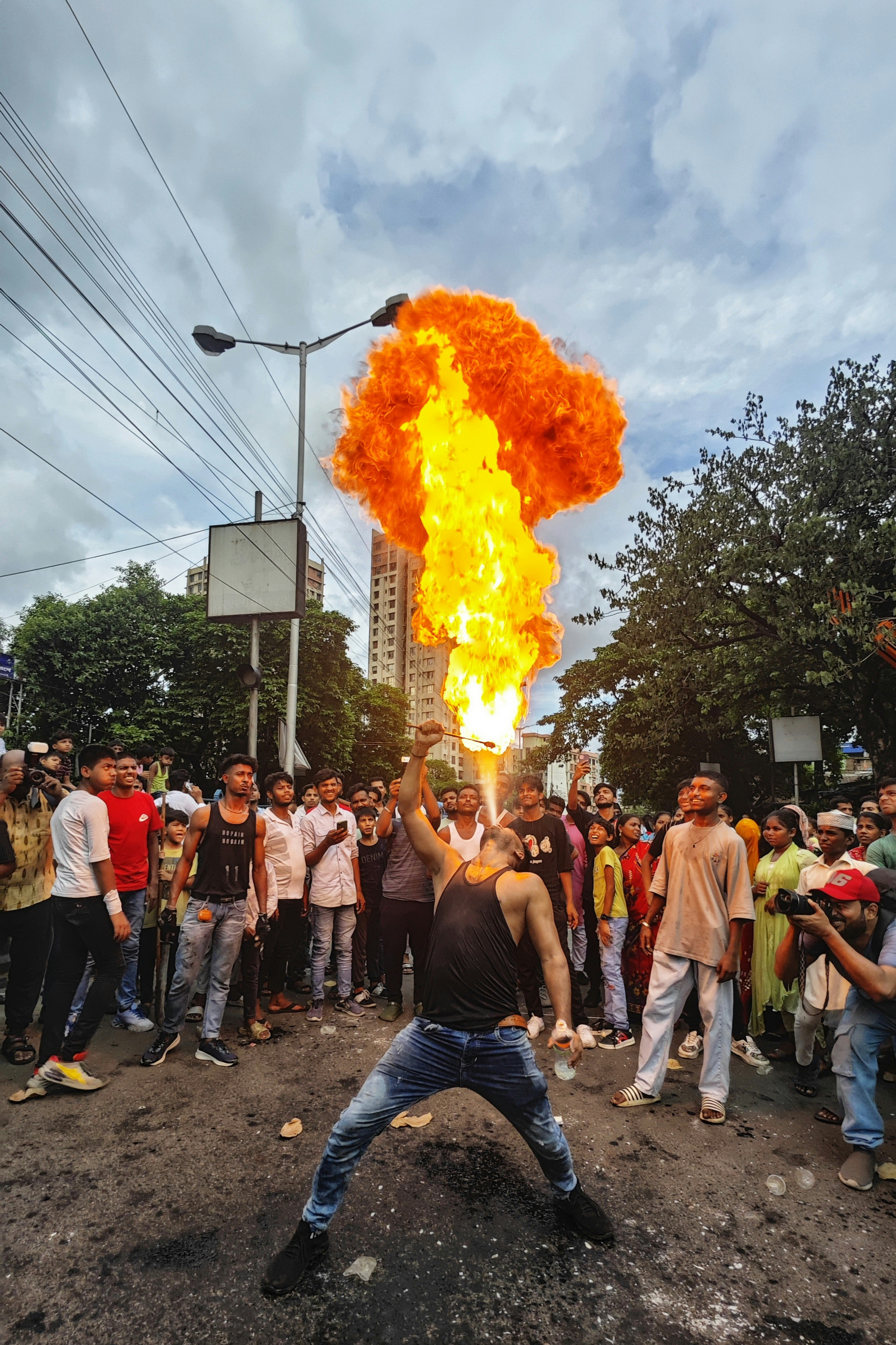 A fire performer unleashes a dramatic plume of flames amidst a captivated crowd in a bustling city street.