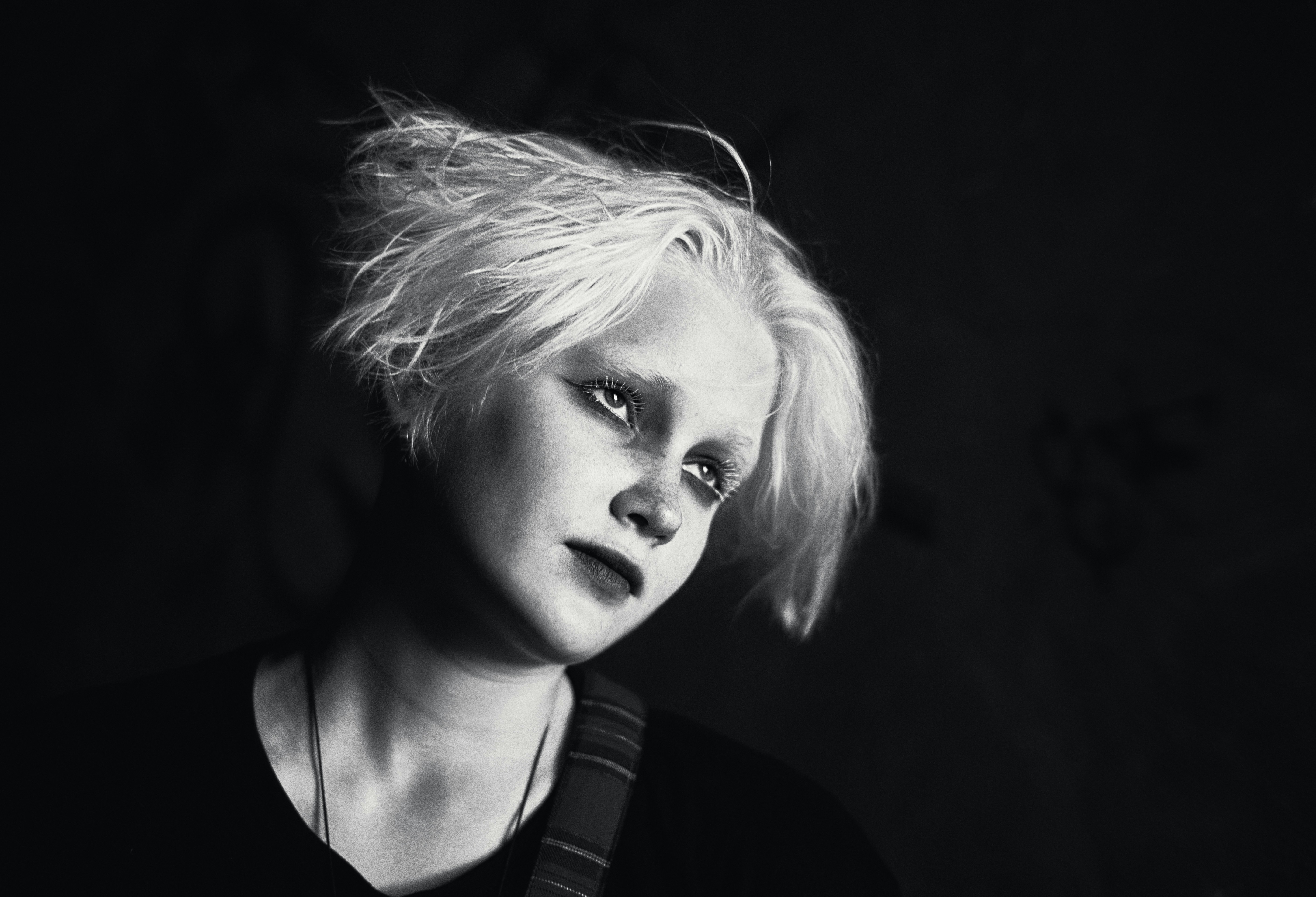 Young person with white hair gazing thoughtfully in a dimly lit setting.