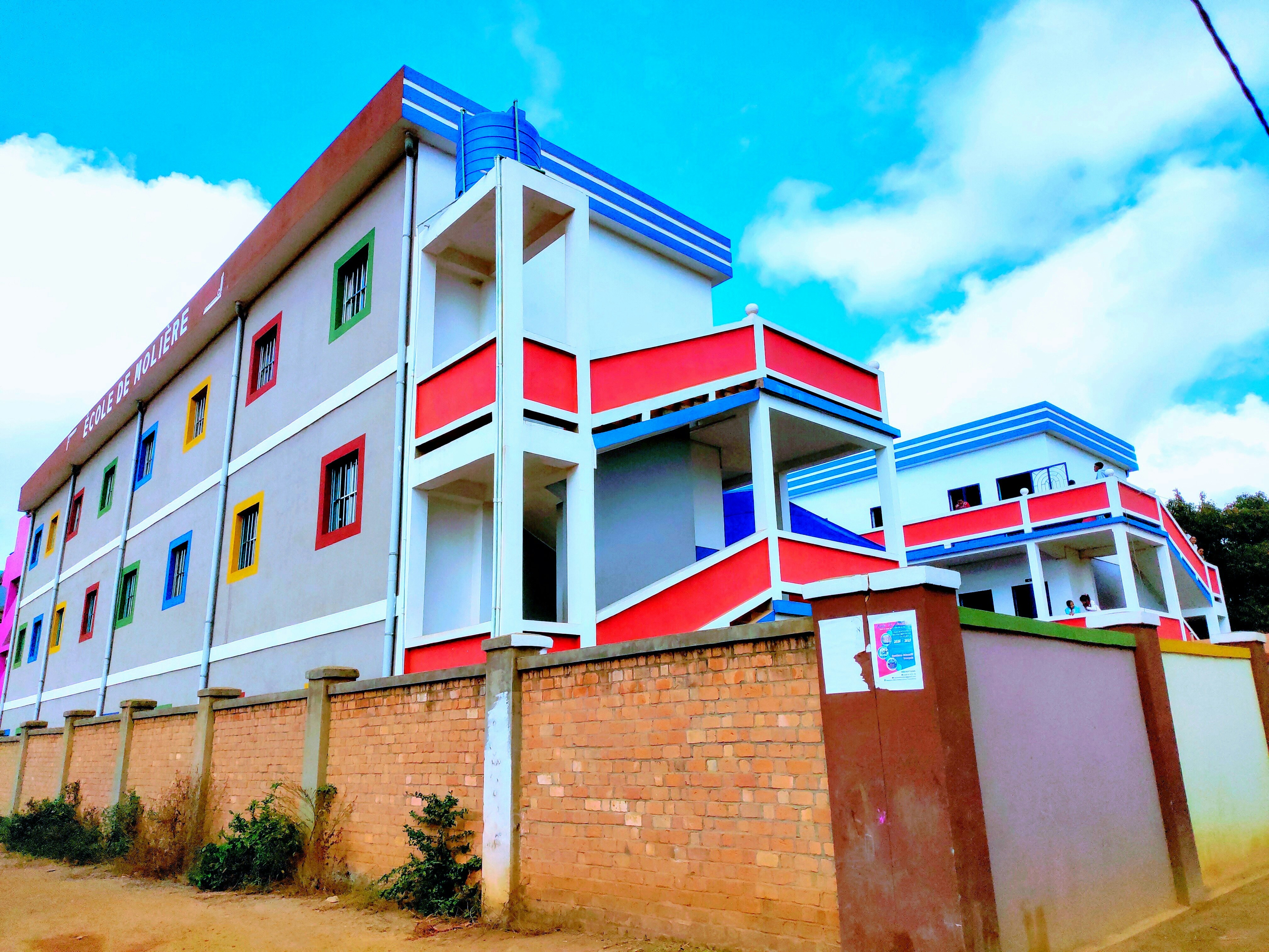A multi - colored building with a brick fence around it photo – Free ...