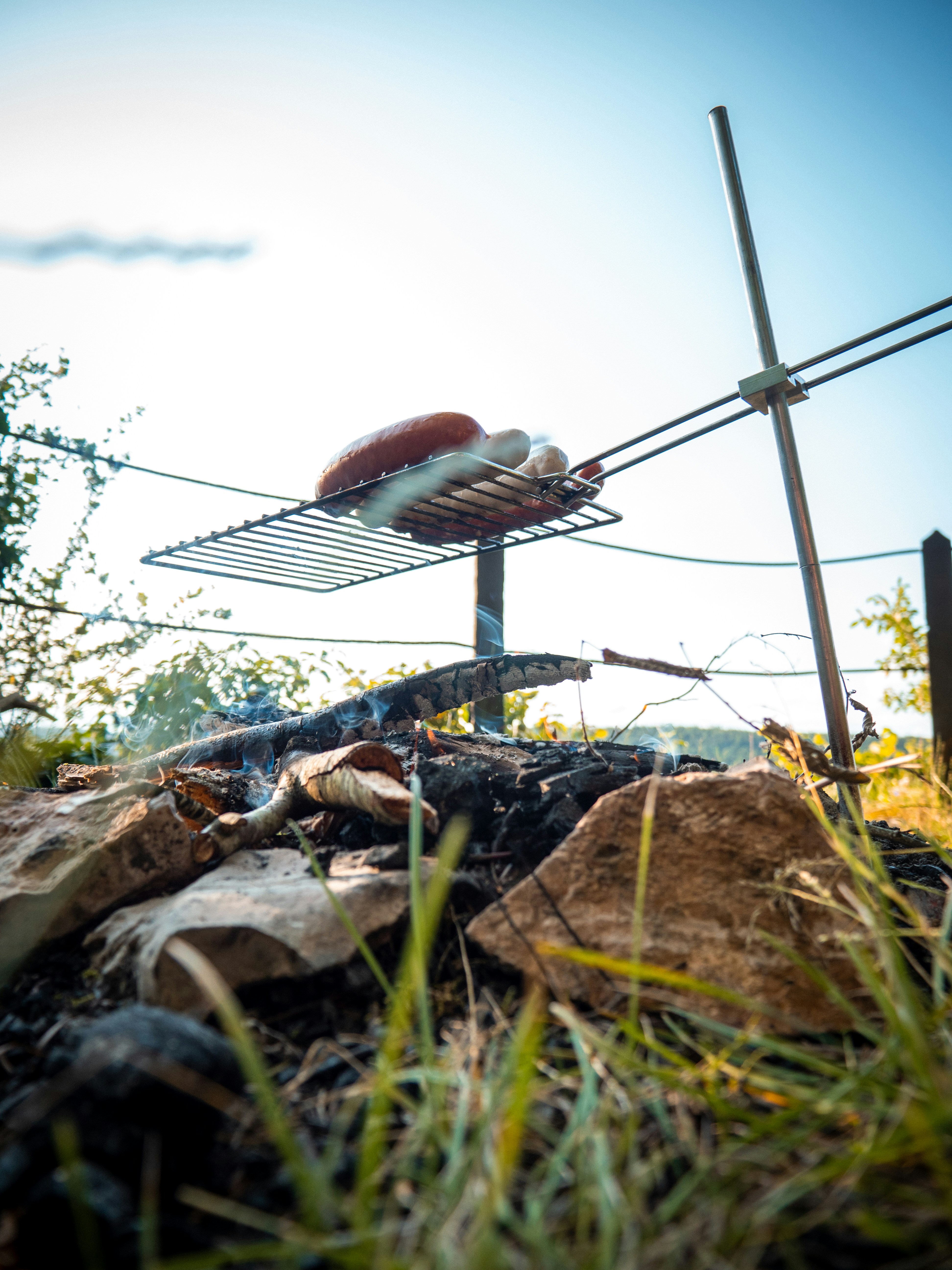 Sizzling grill on a metal rack above a campfire under a wire frame wake of dawn