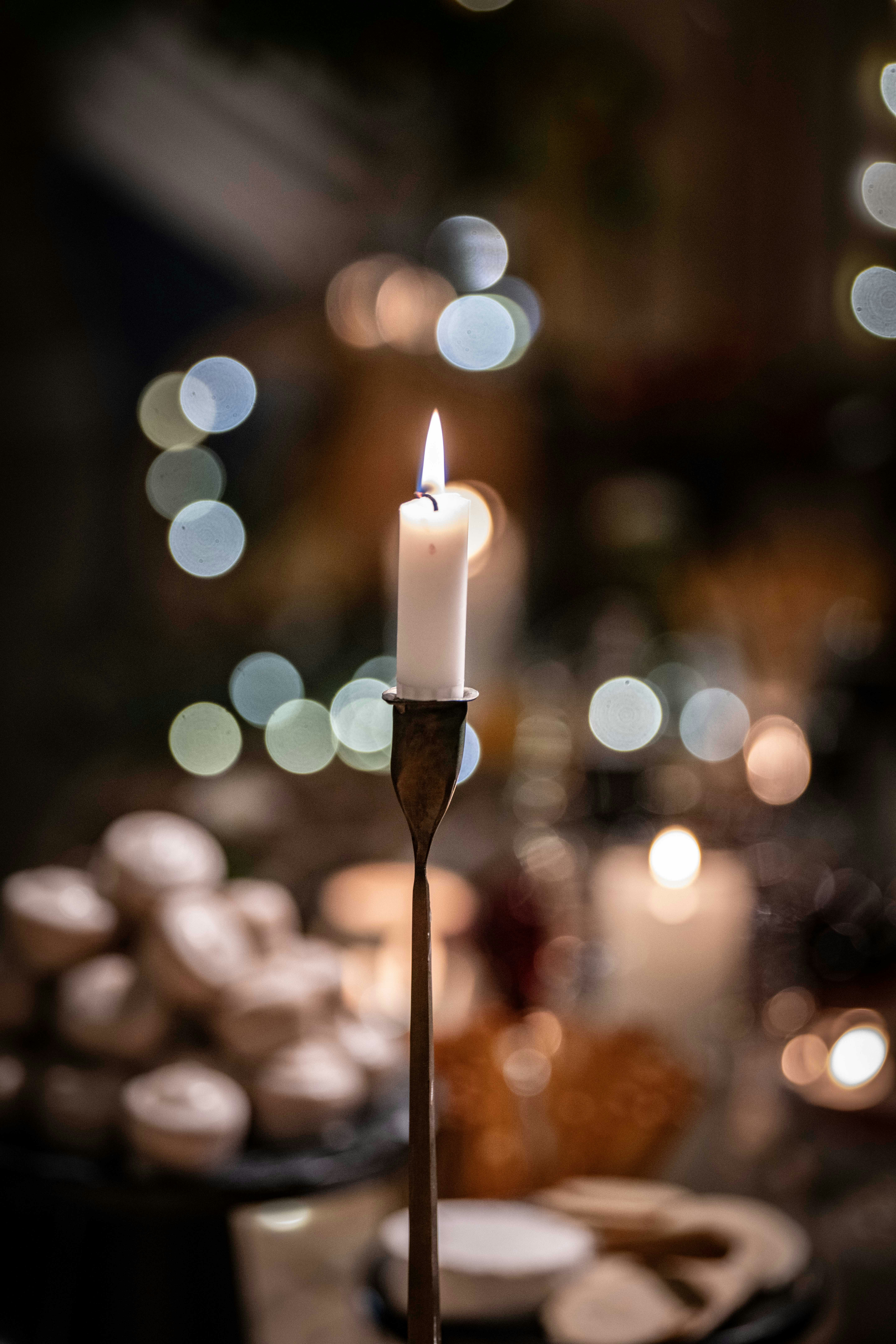 A lit candle stands tall amidst a blurred background of festive lights and treats, creating a warm, inviting atmosphere.