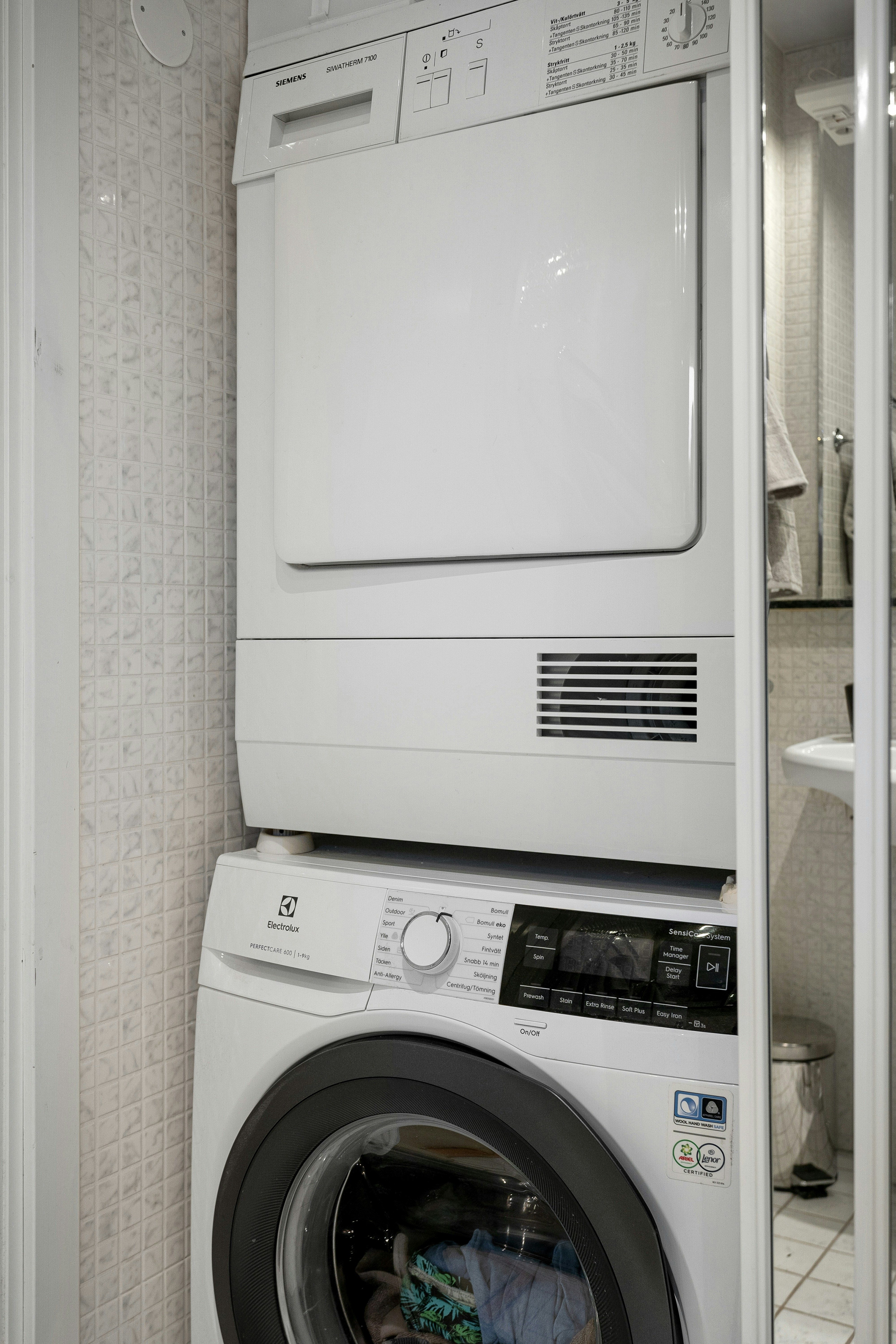 Symmetry in White: A Compact Laundry Stack in a Tiled Nook