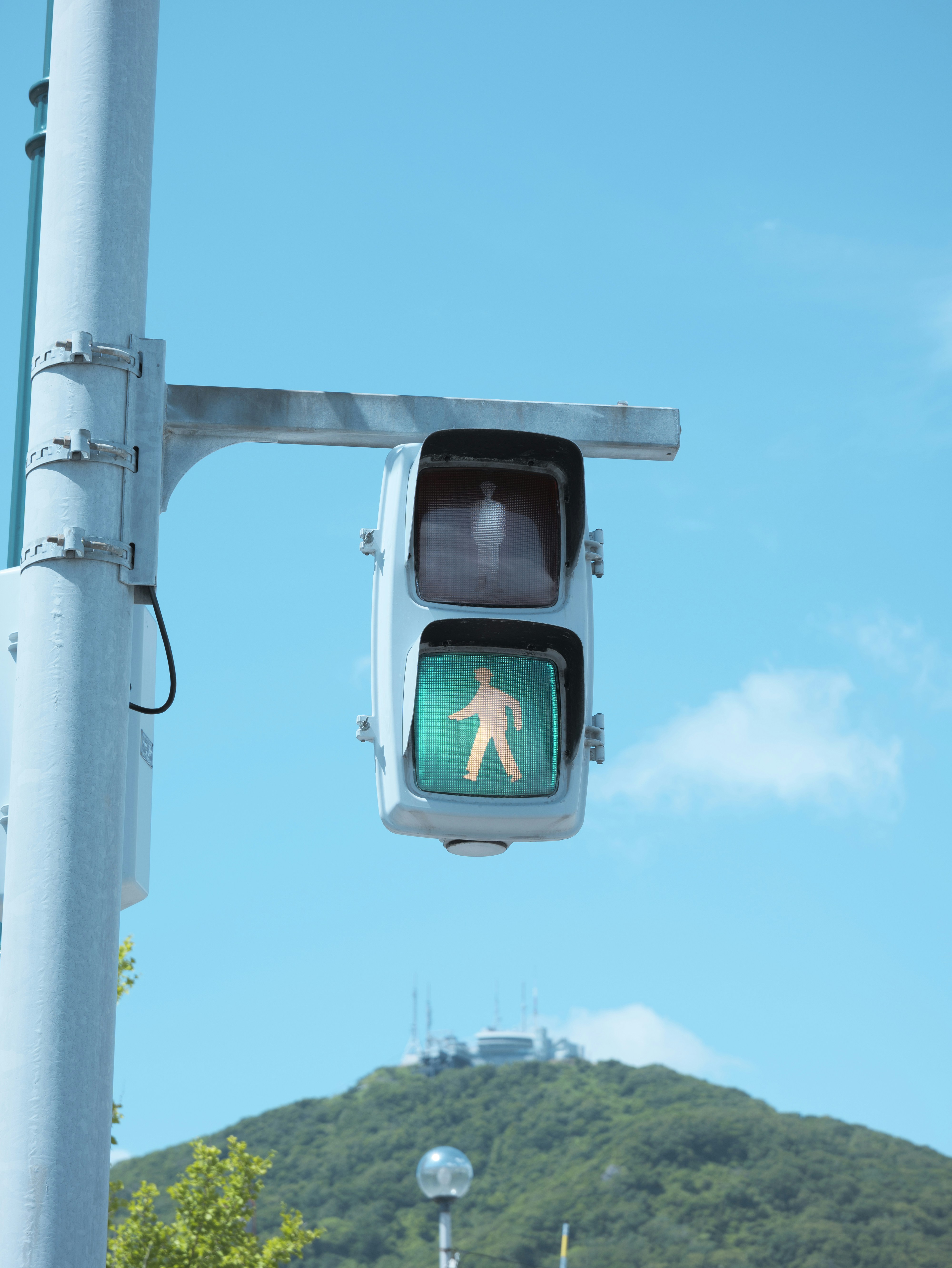 Green Pedestrian Signal Framed by a Bright Sky Over a Hill