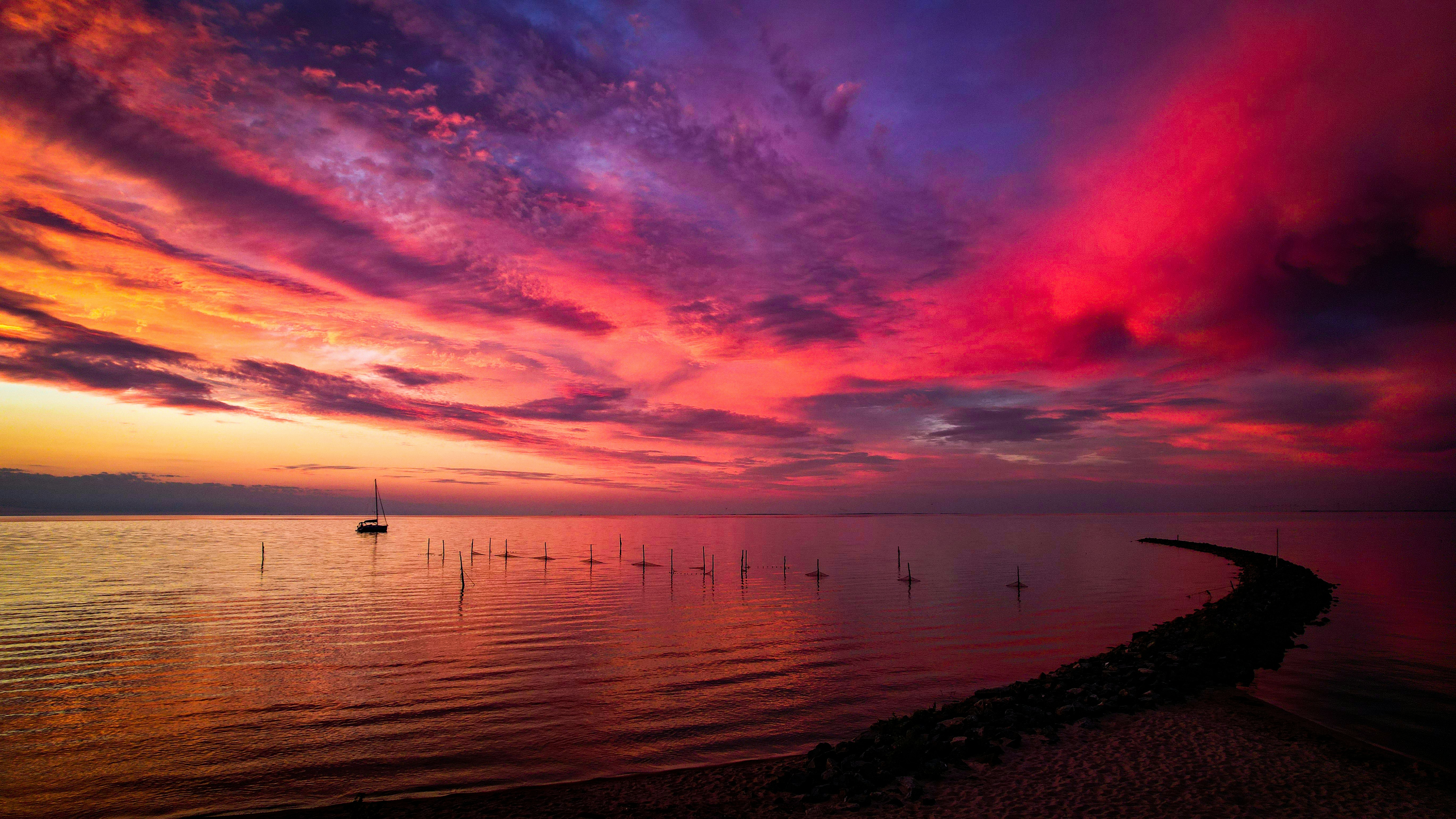 Lone Sailboat Beneath Fiery Dusk Over a Curved Breakwater