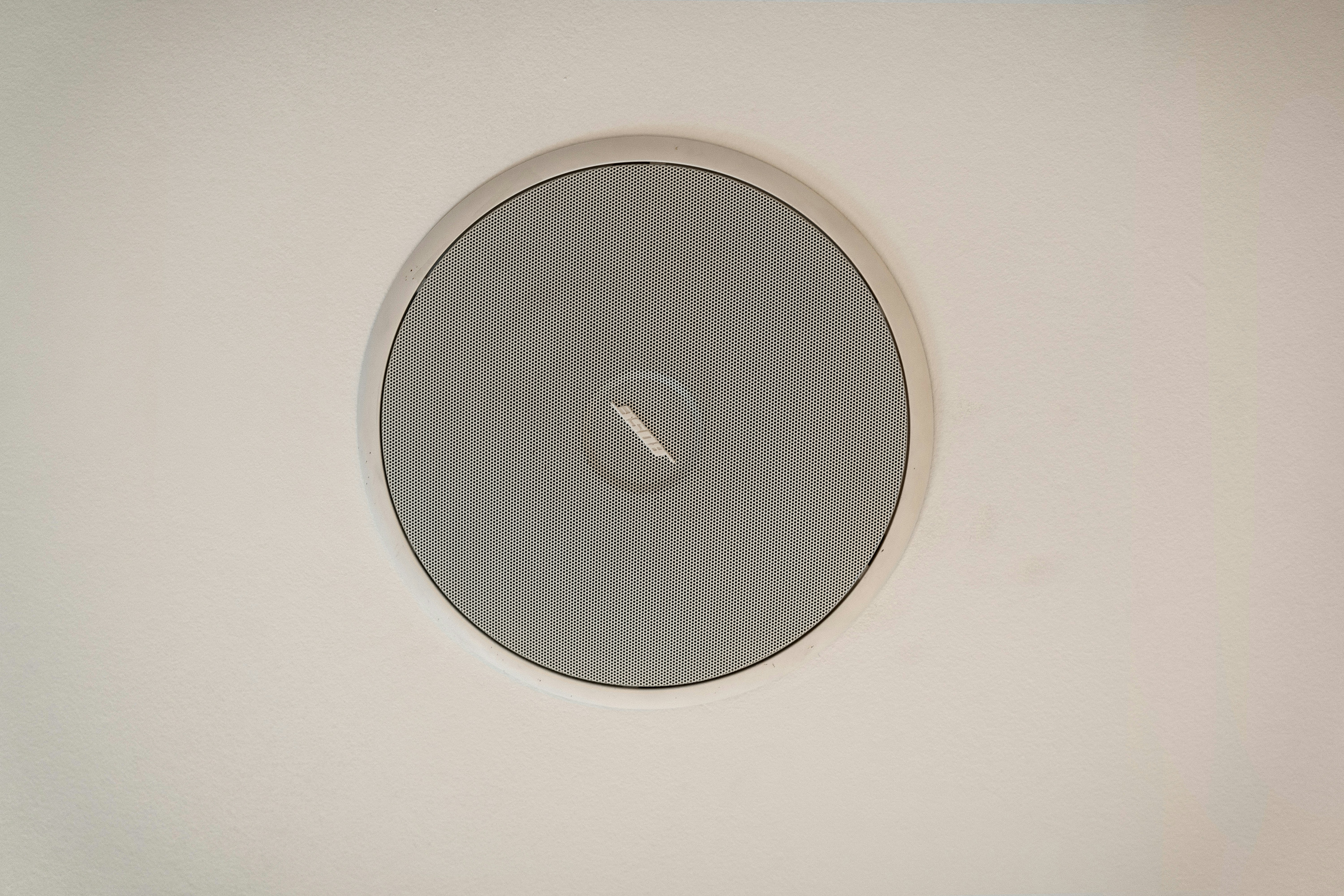 A sleek, circular ceiling speaker blends seamlessly into a minimalist interior. Its understated design complements the surrounding space.
