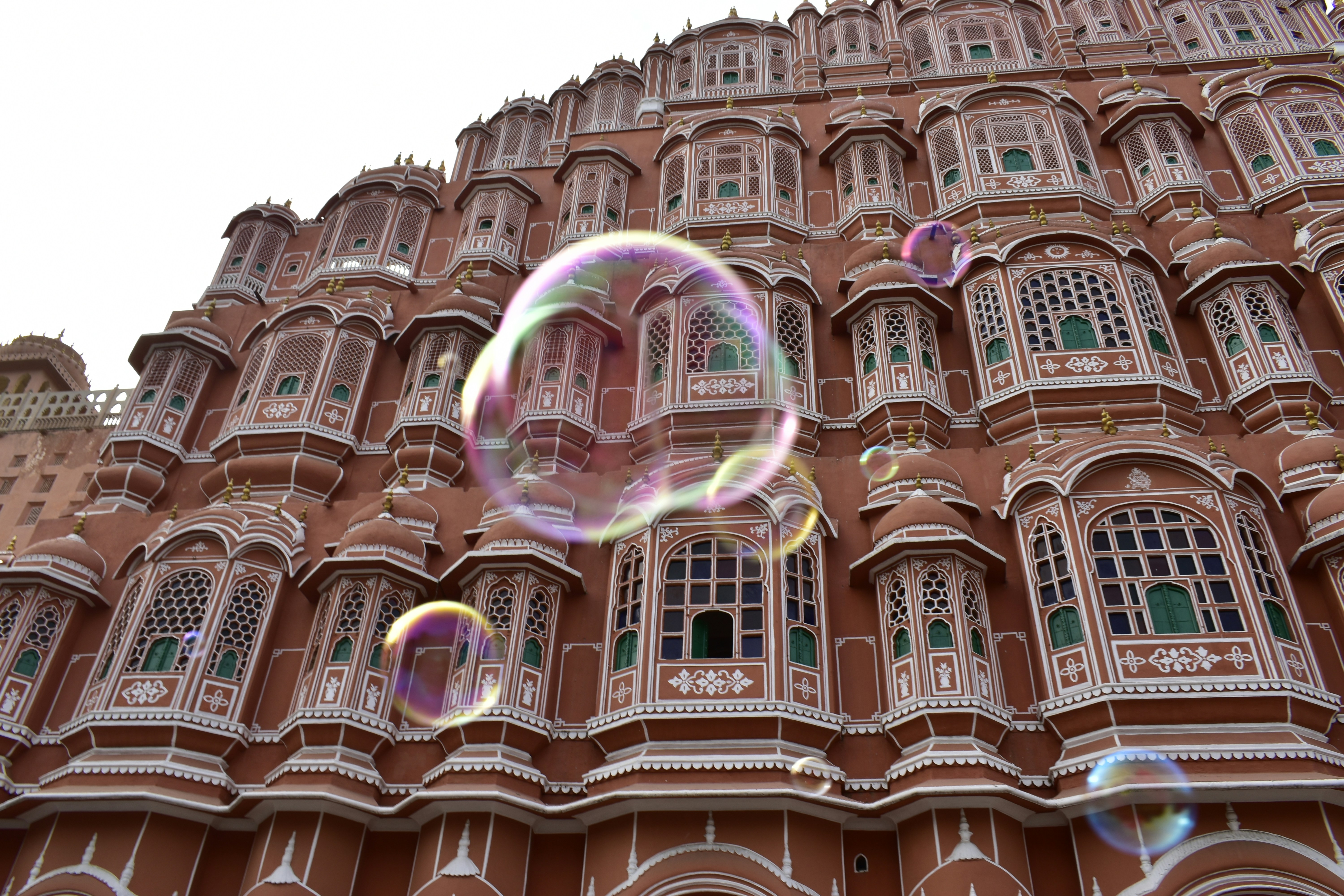 Colorful bubbles float in front of an ornate pink building with arched windows and decorative white trim.