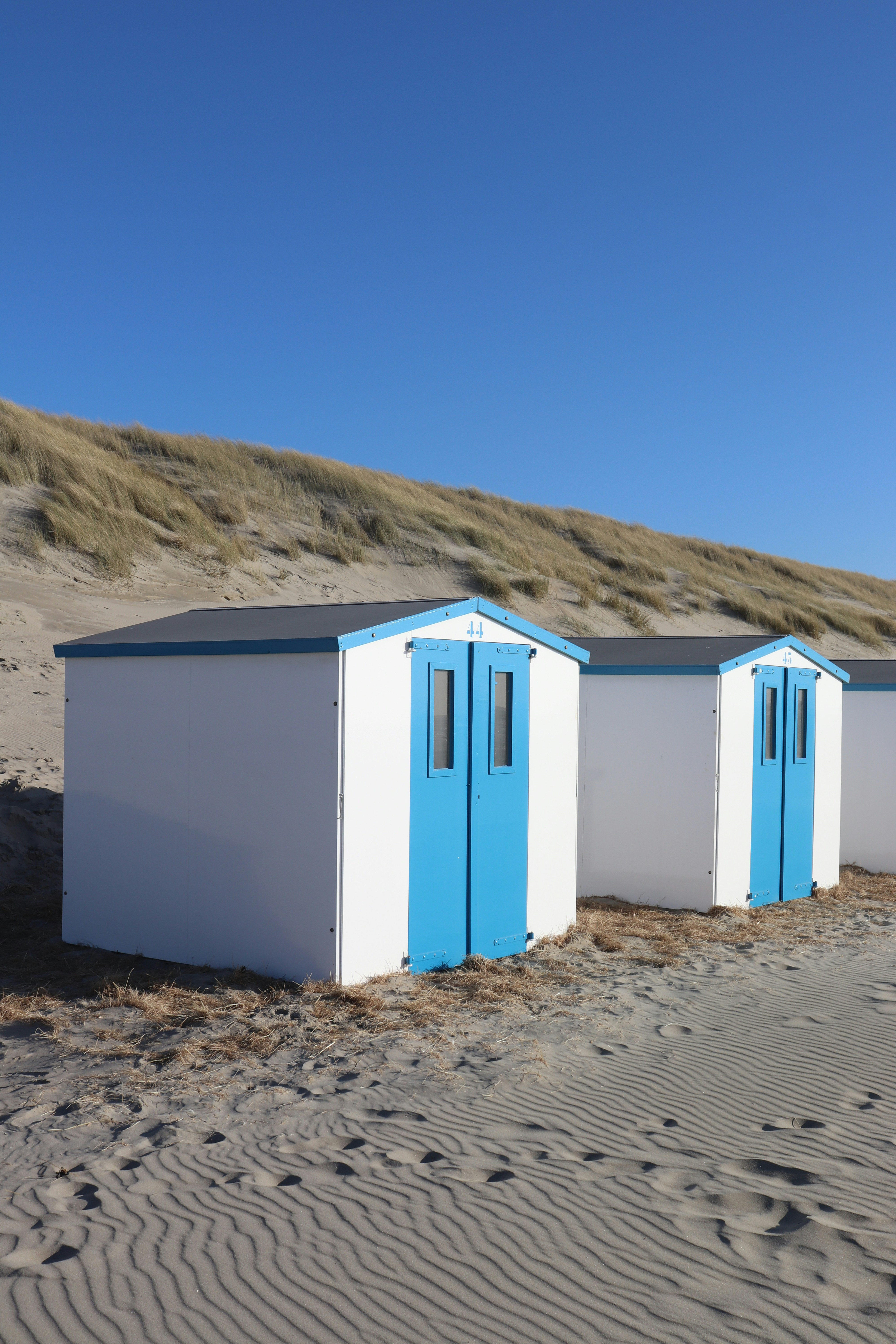Blue Doors on White Beach Huts: Dune-Line Minimalism at Noon