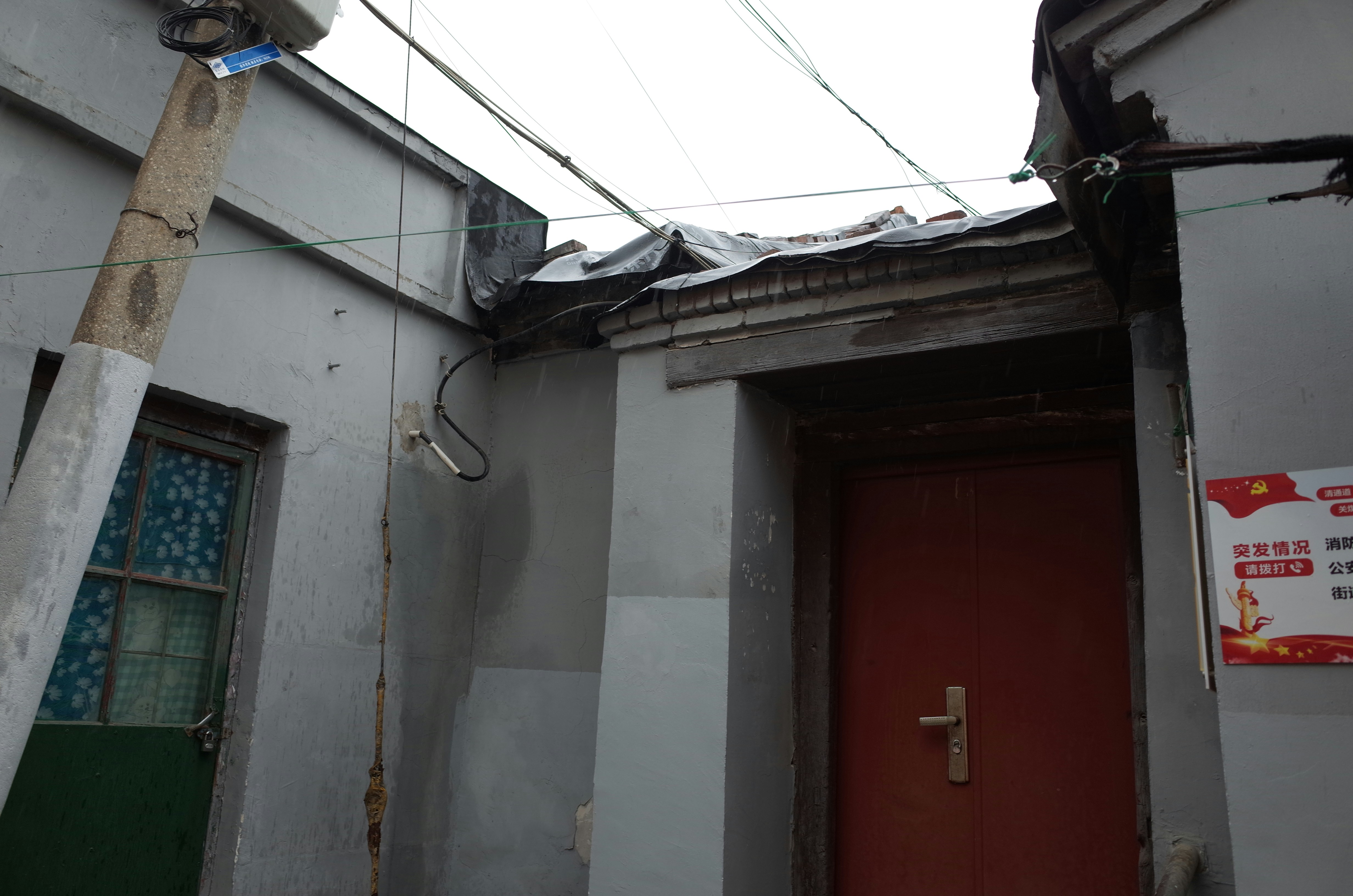 Gray, weathered courtyard with a closed red door beneath a tangle of overhead wires. This photograph emphasizes urban decay and utilitarian architecture.