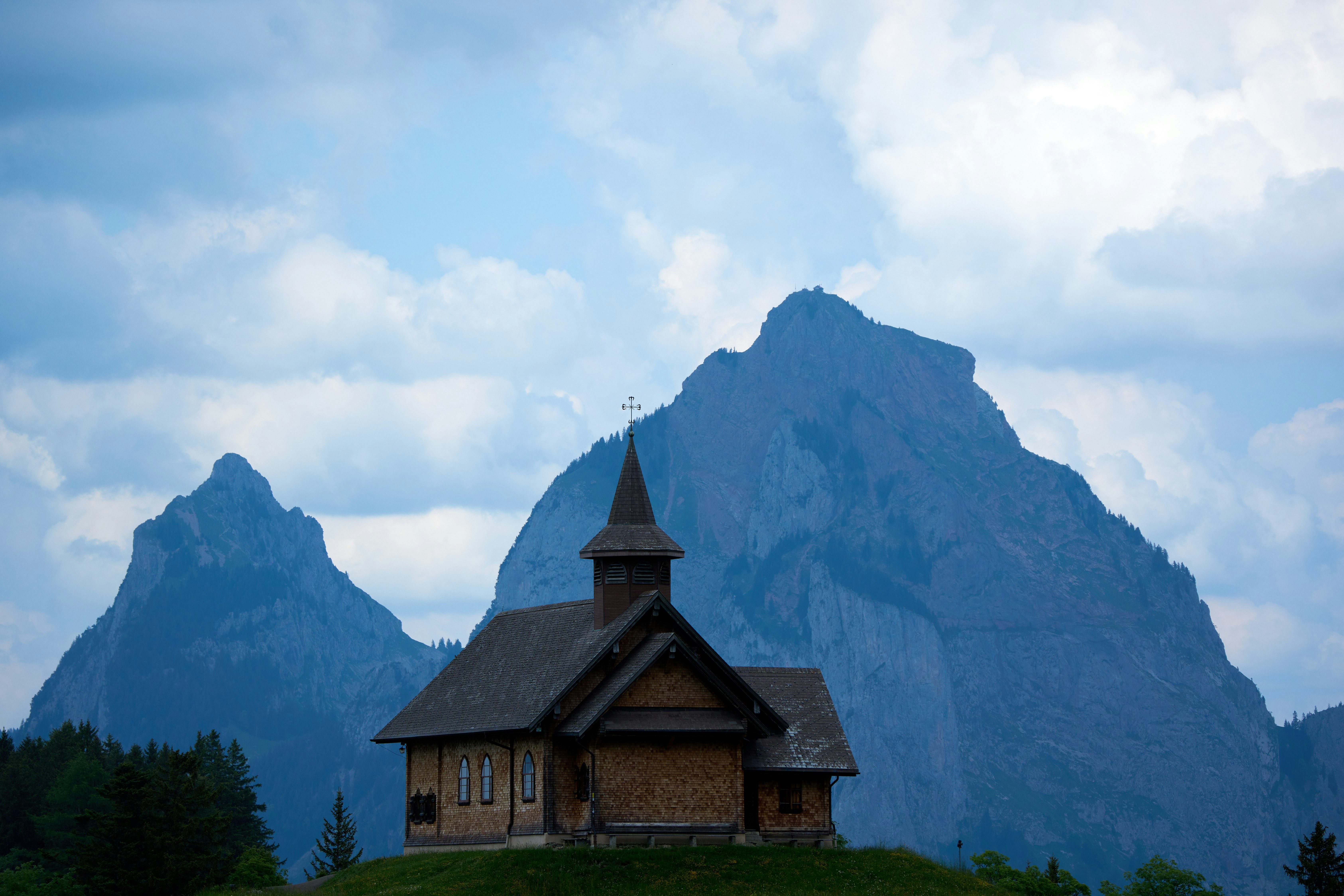 A small church on a grassy hill with mountains in the background photo ...