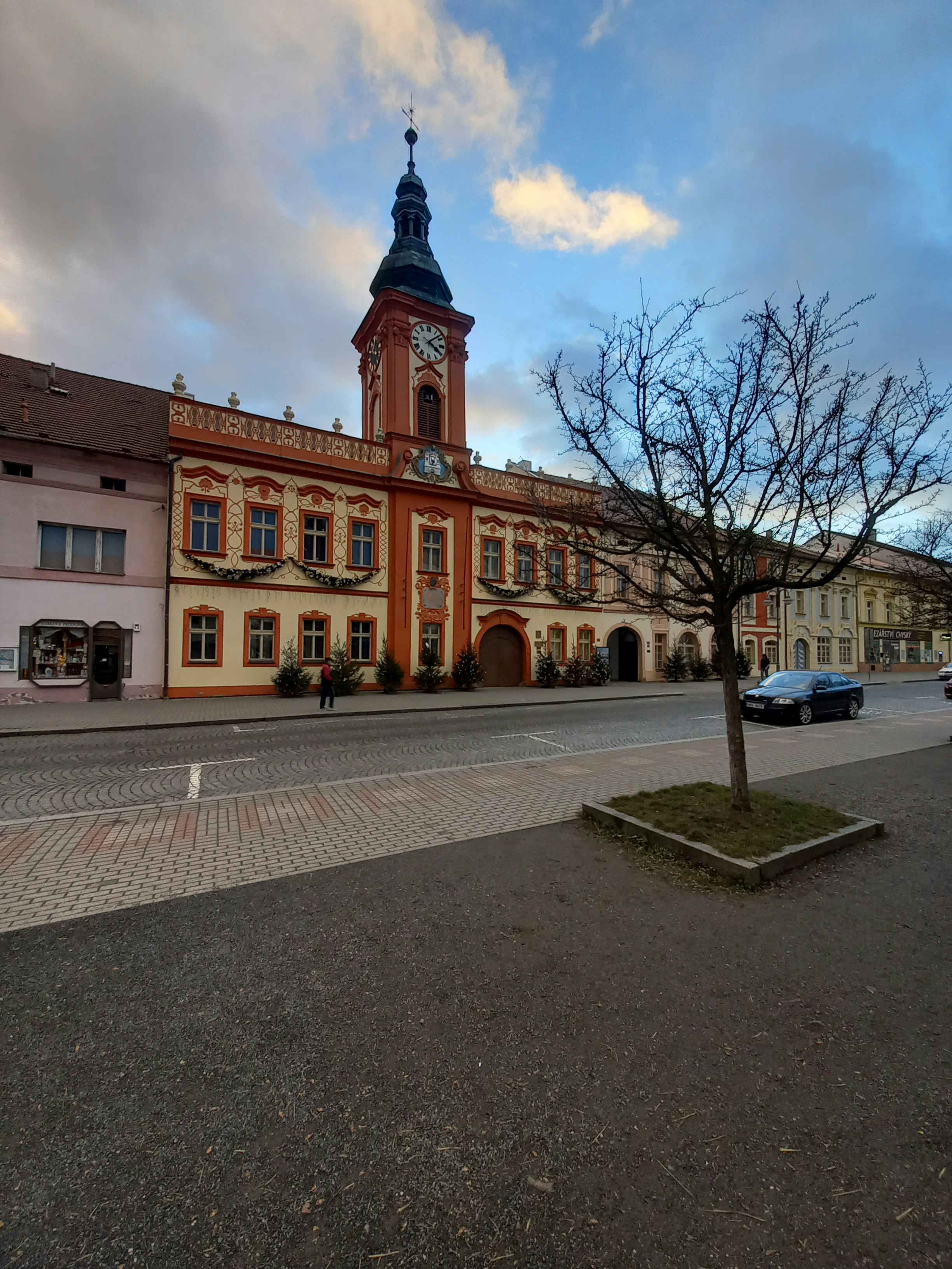 Historic clock tower and vibrant building facade in a quaint town square, framed by a bare tree. 