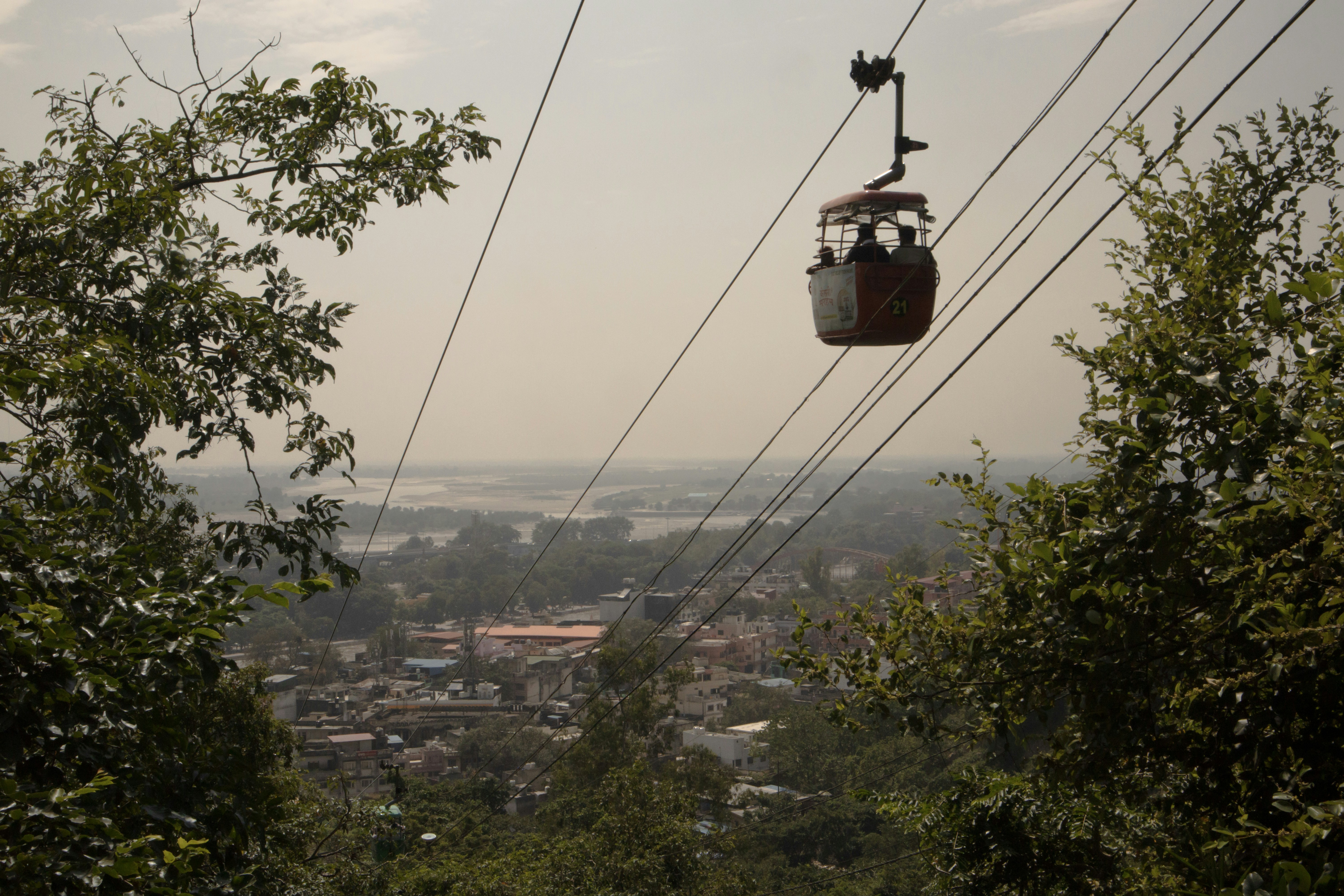 A gondola glides through the air, framed by lush greenery, offering a panoramic view of the sprawling town below. The distant horizon reveals a serene body of water.