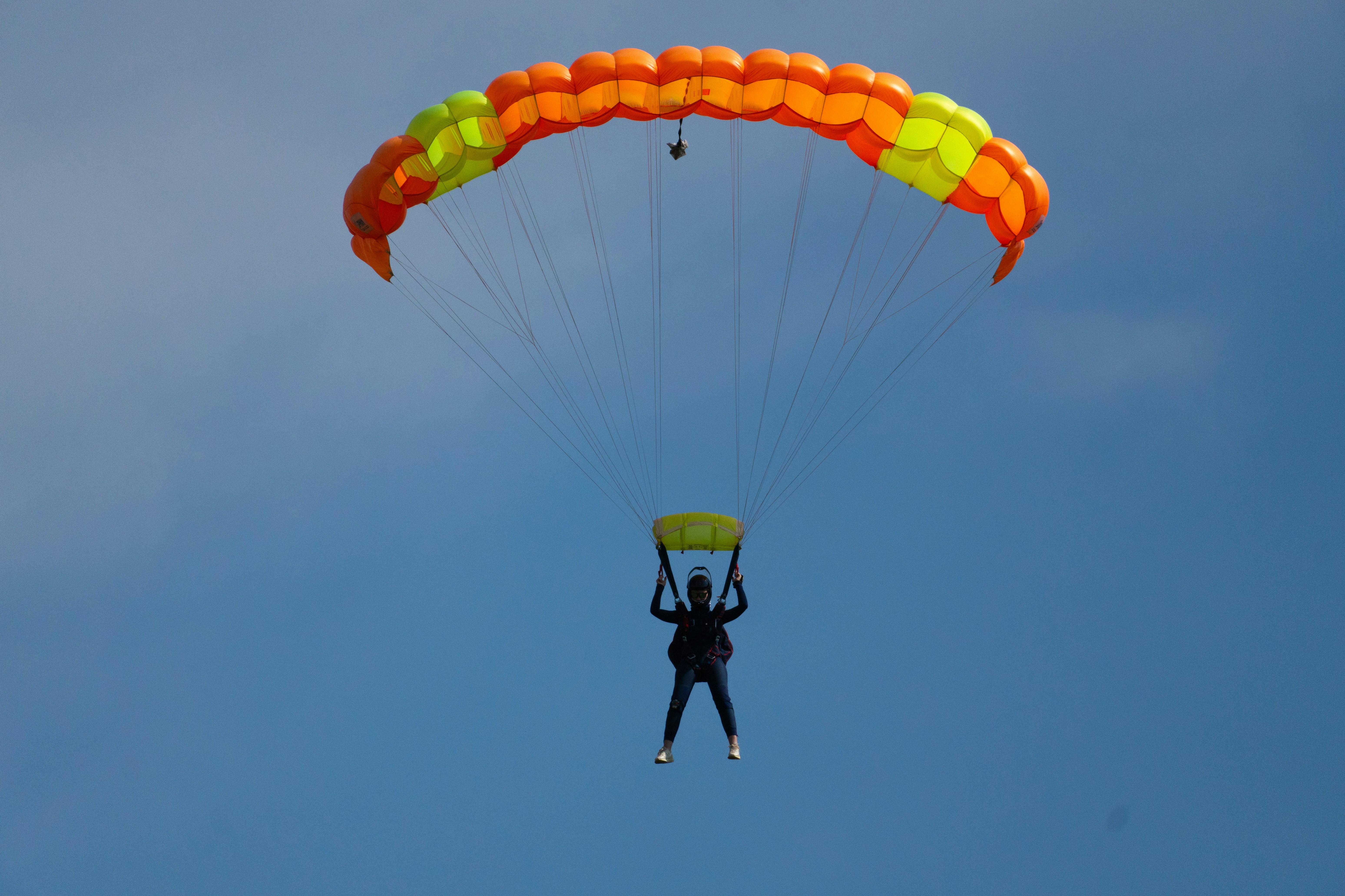Mid-air Silhouette: Parachute Descent Against a Clear Blue Sky