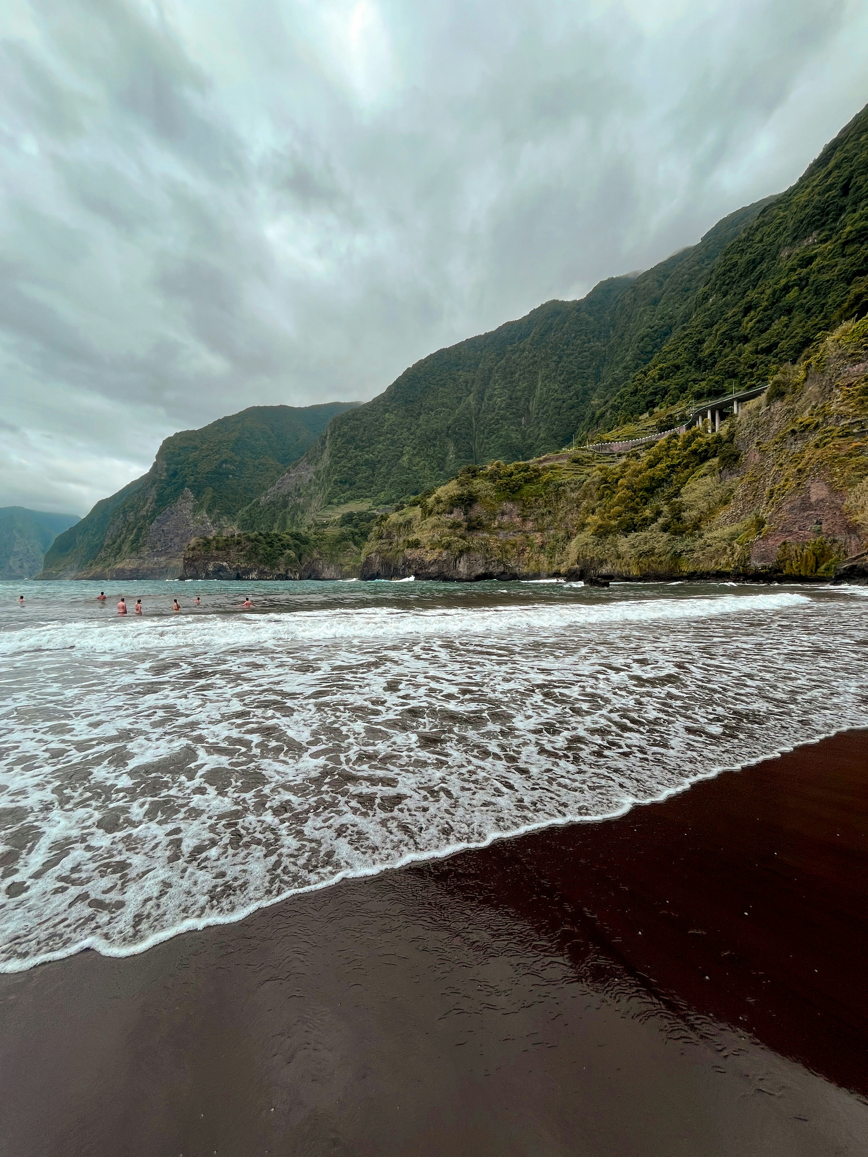 Black-Sand Coastline under Cloudy Cliffs and a Winding Road