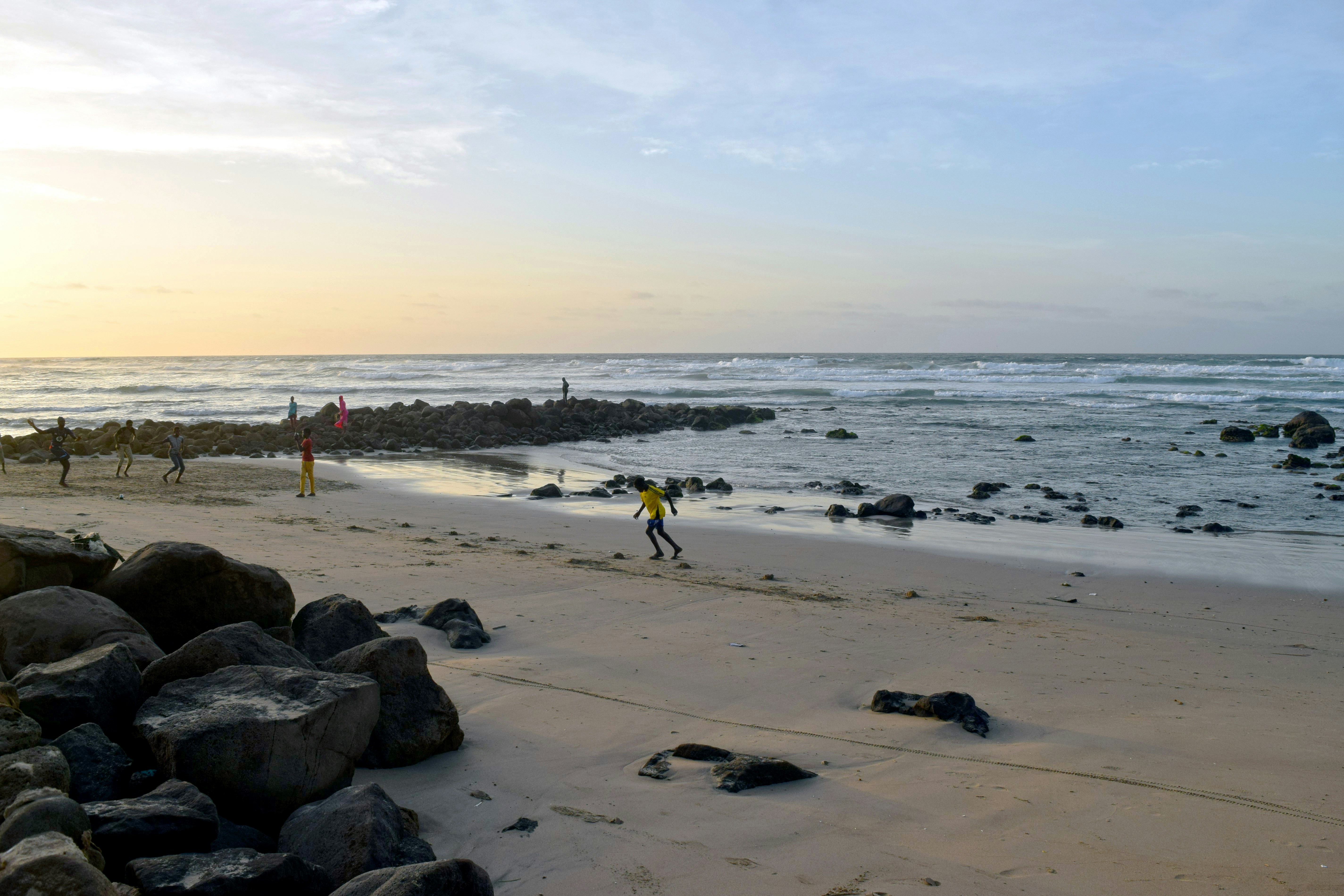 Children playing soccer on Virage beach in Dakar against a backdrop of ocean waves and a setting sun.