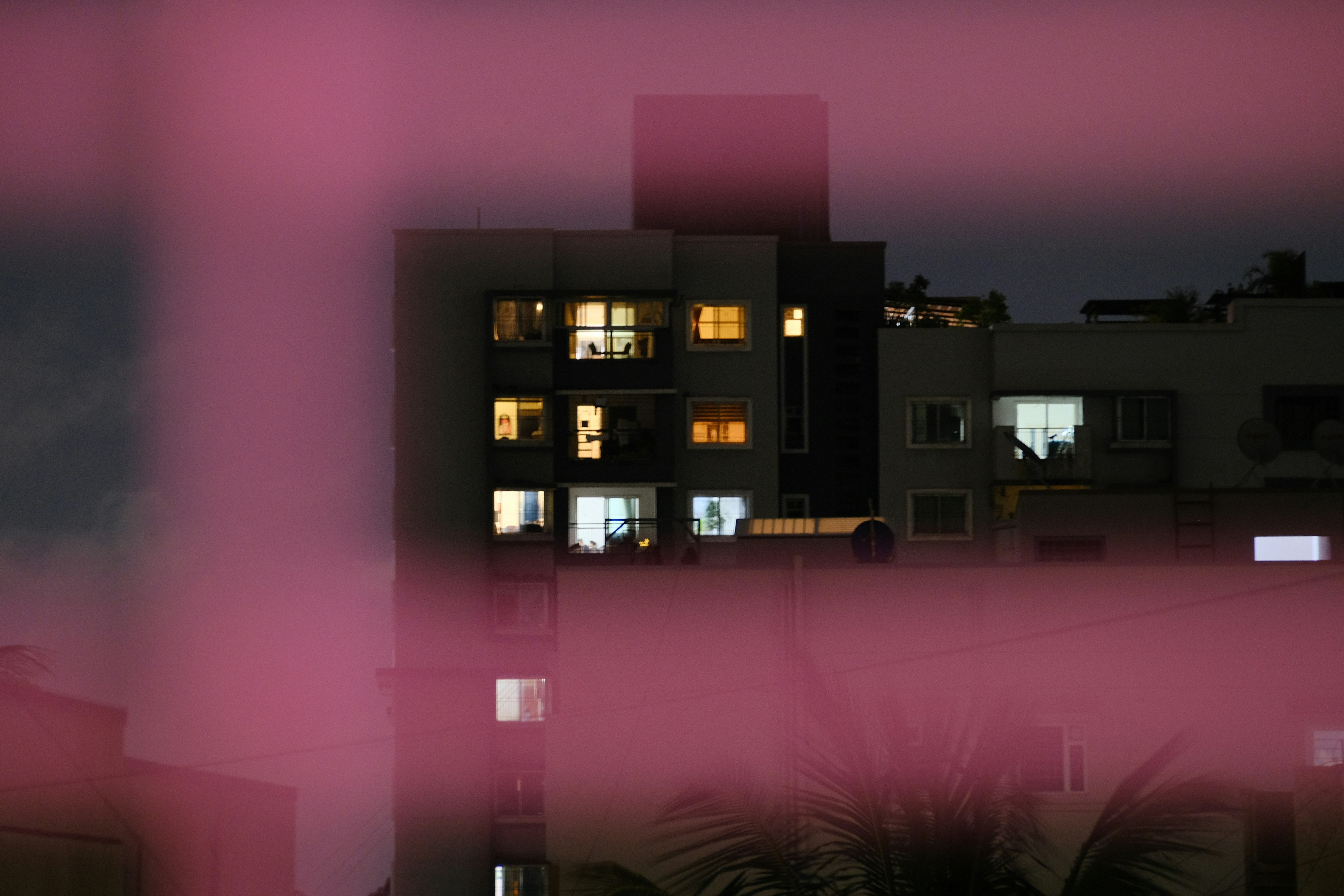 View of a faraway building on a summer night through a grilled window lit in pink
