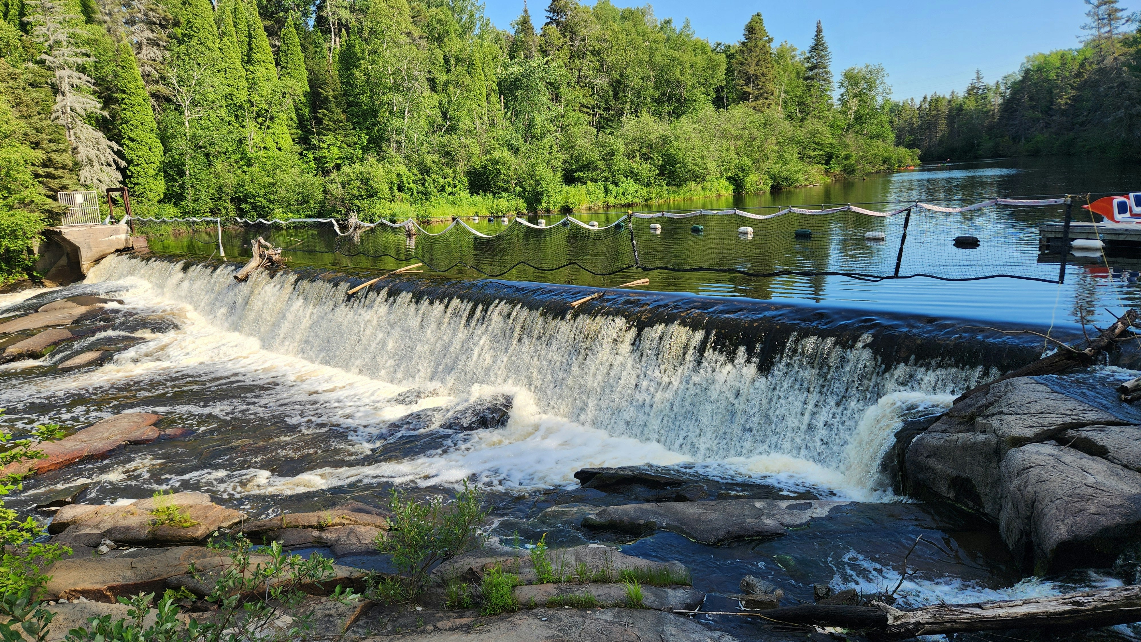 Waterfall cascading over rocks surrounded by lush greenery under a clear blue sky.