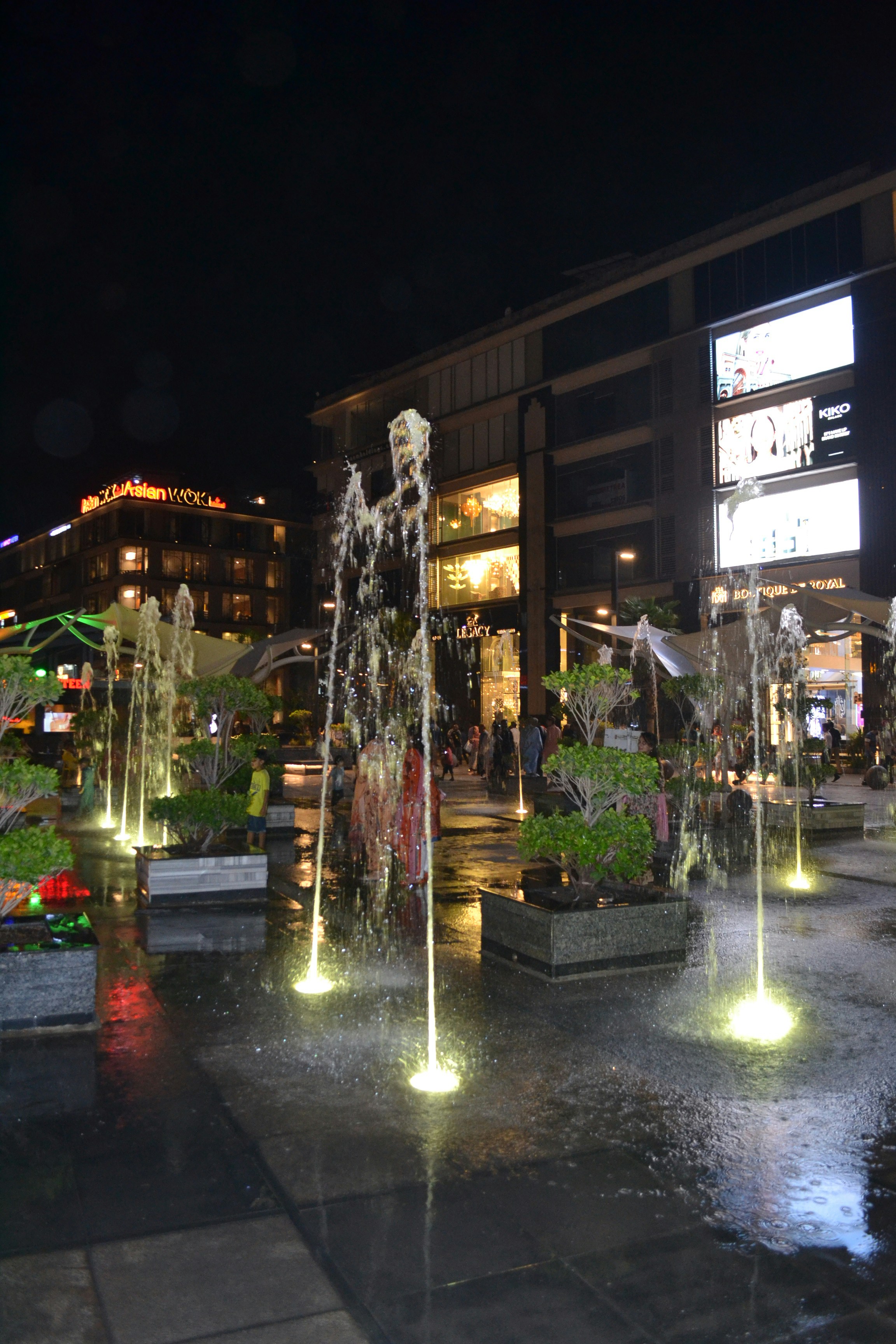 A group of fountains in a city square at night photo – Free Building ...