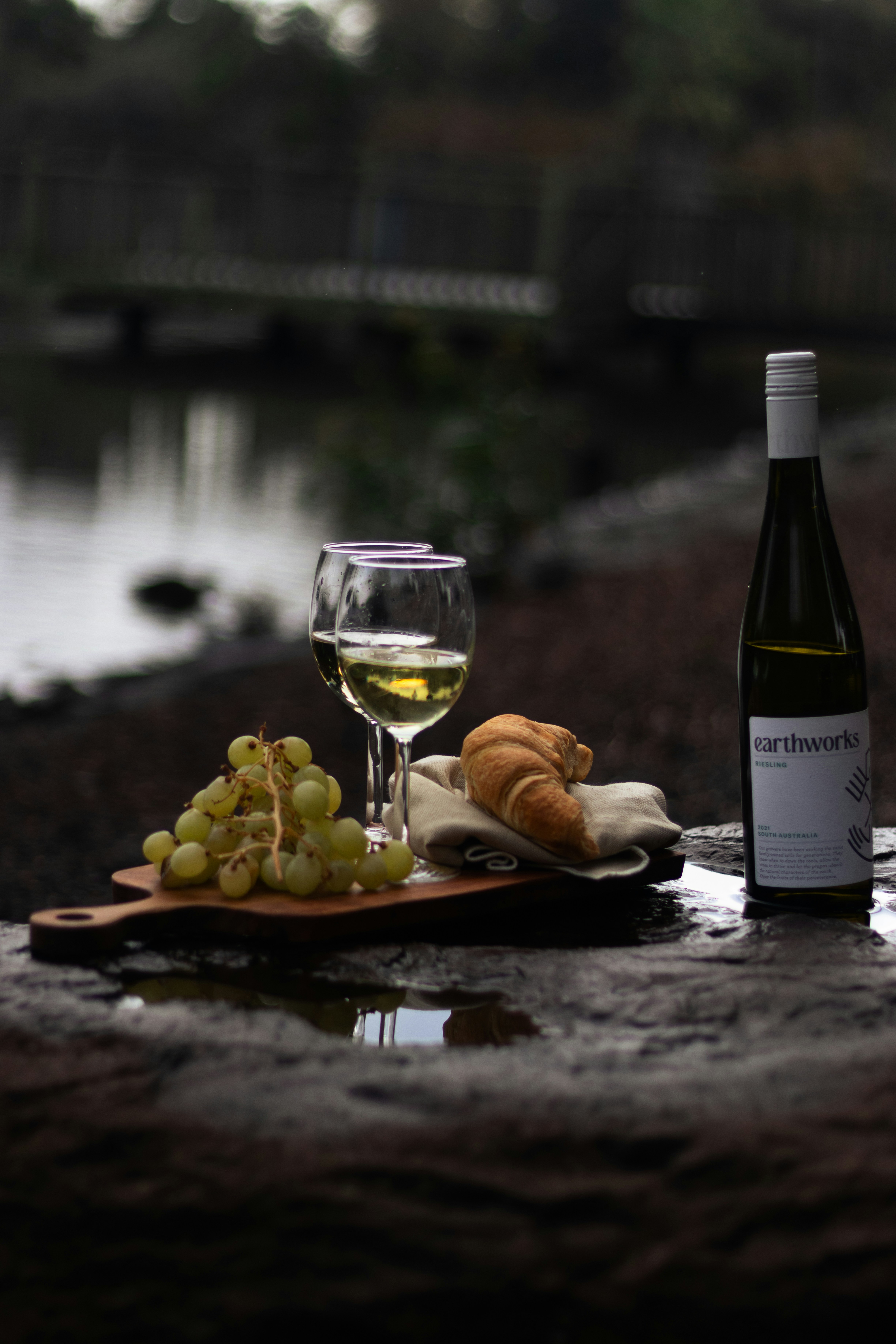 Still Life by the Water: Wine, Wine Glass, and Pastry on a Riverbank