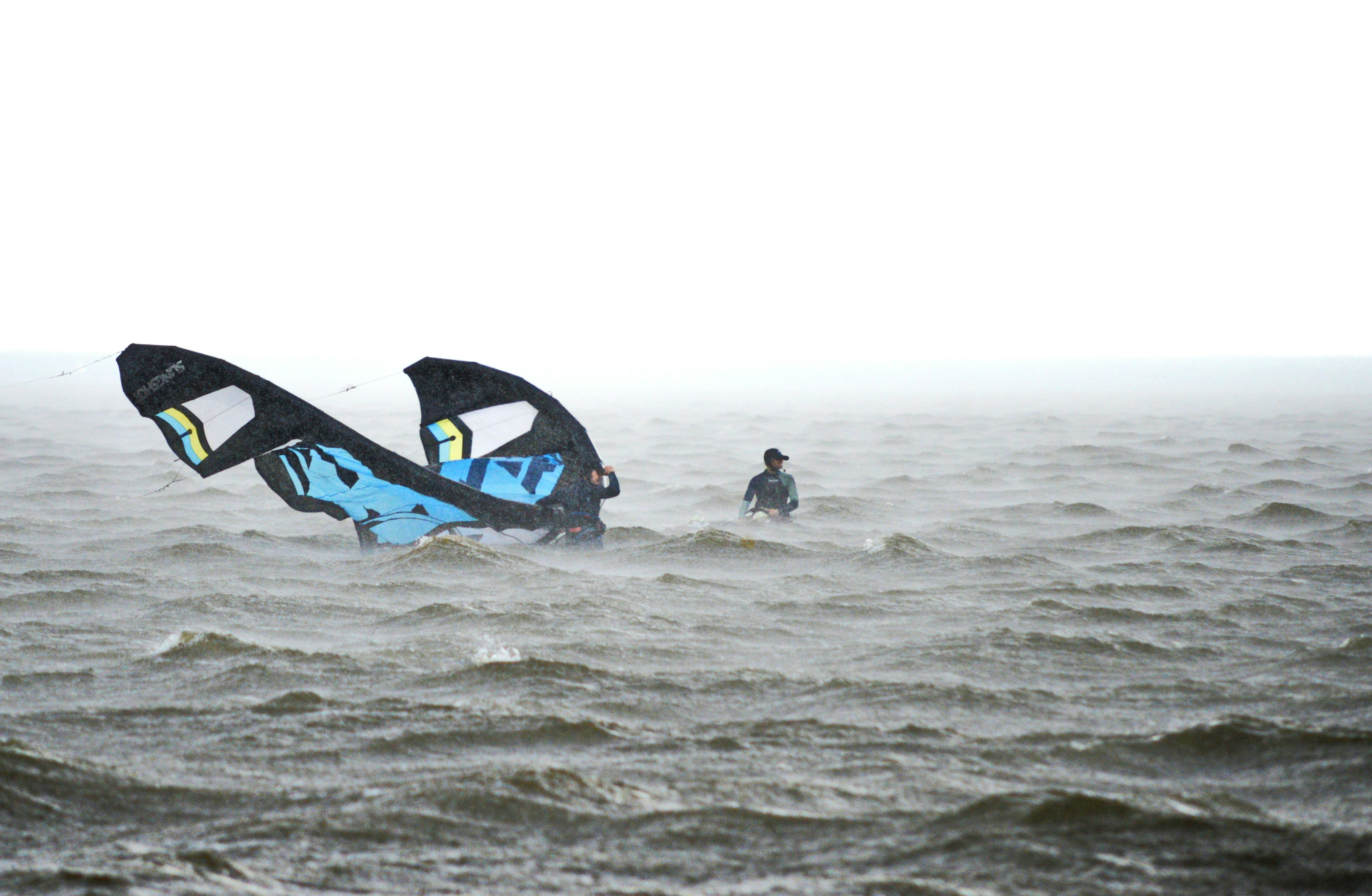 Windswept Wake: Kite Surfer and Helper Amid Rough Sea