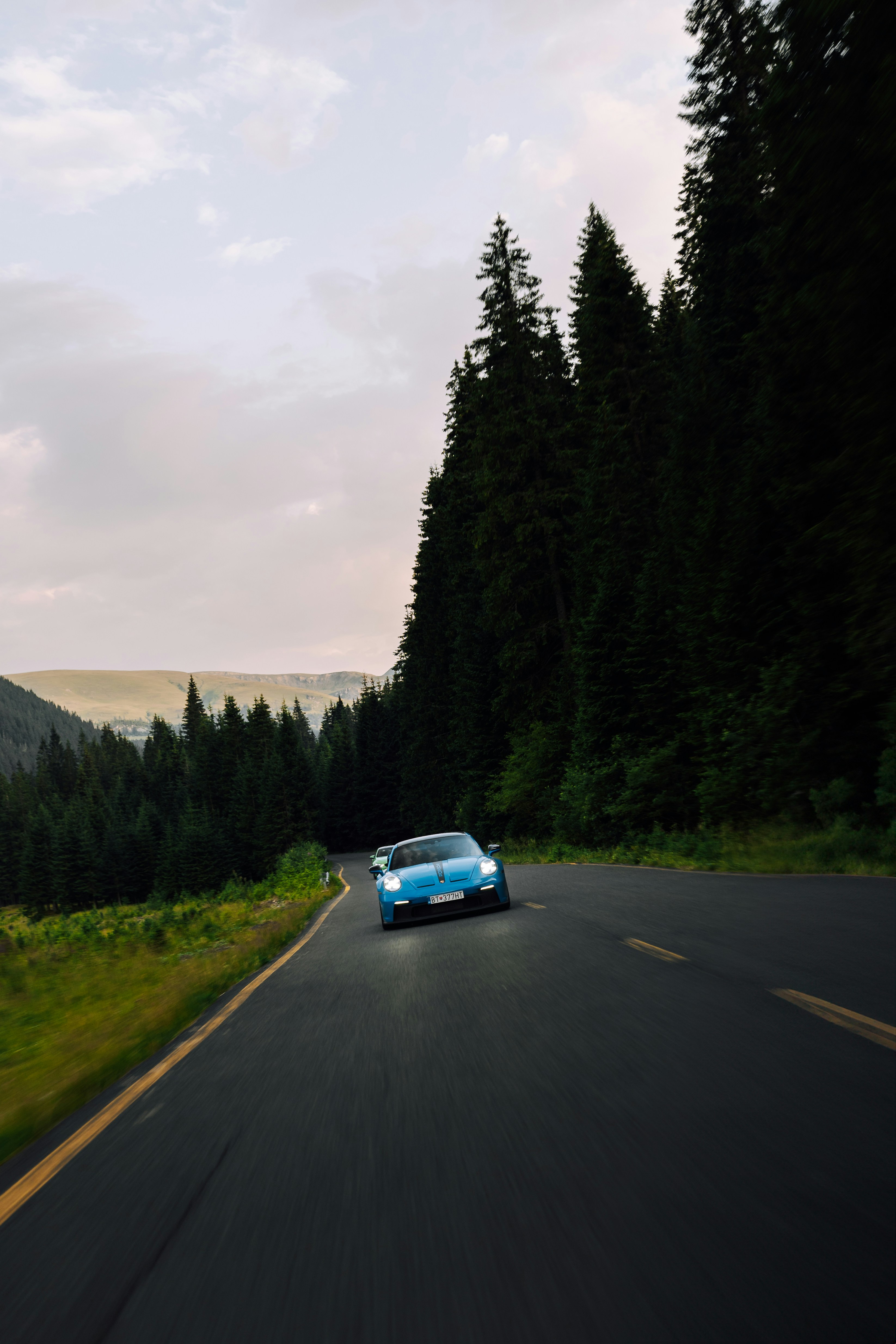A blue car driving down a road next to a forest photo – Free Road Image ...
