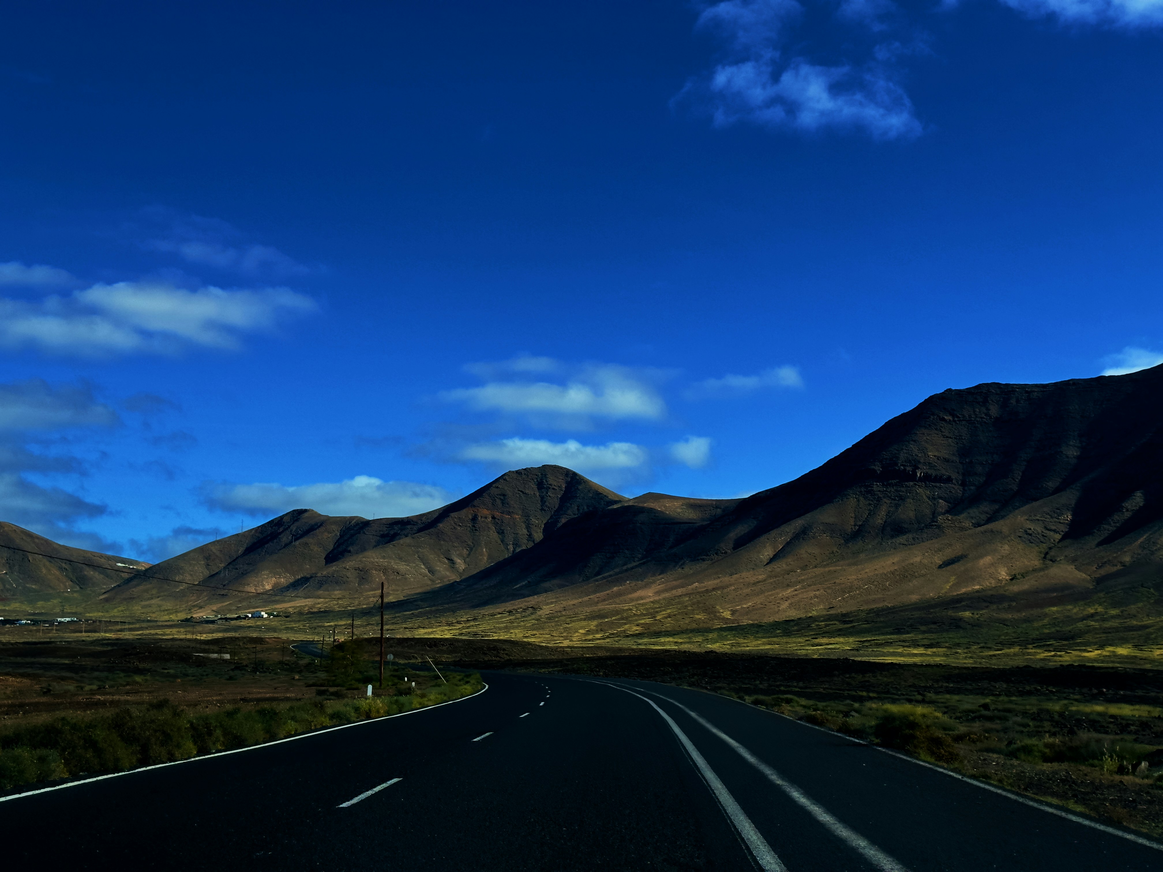 Open road stretching towards distant mountains under a bright blue sky.