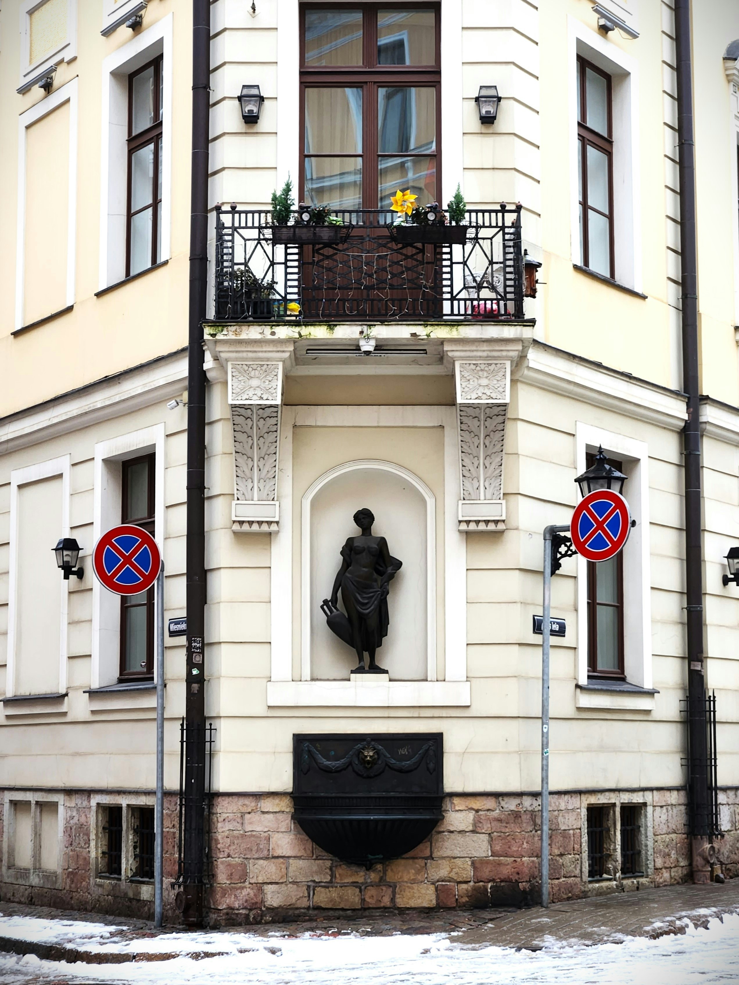 Alcove Sentinel on a Cream Corner: Statue Beneath an Ornate Balcony