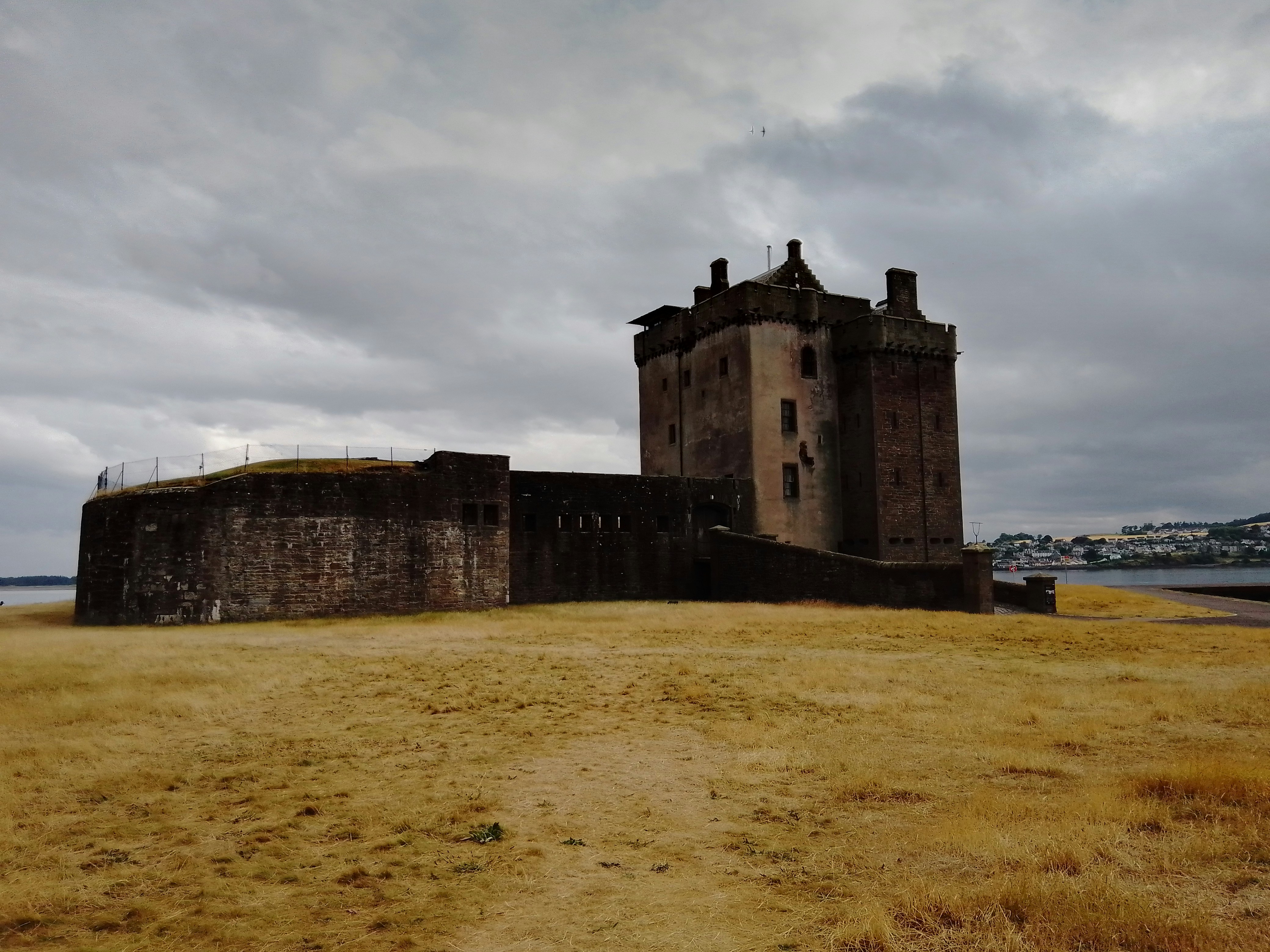 Broughty Castle under a moody sky. | A large castle sitting on top of a dry grass field
