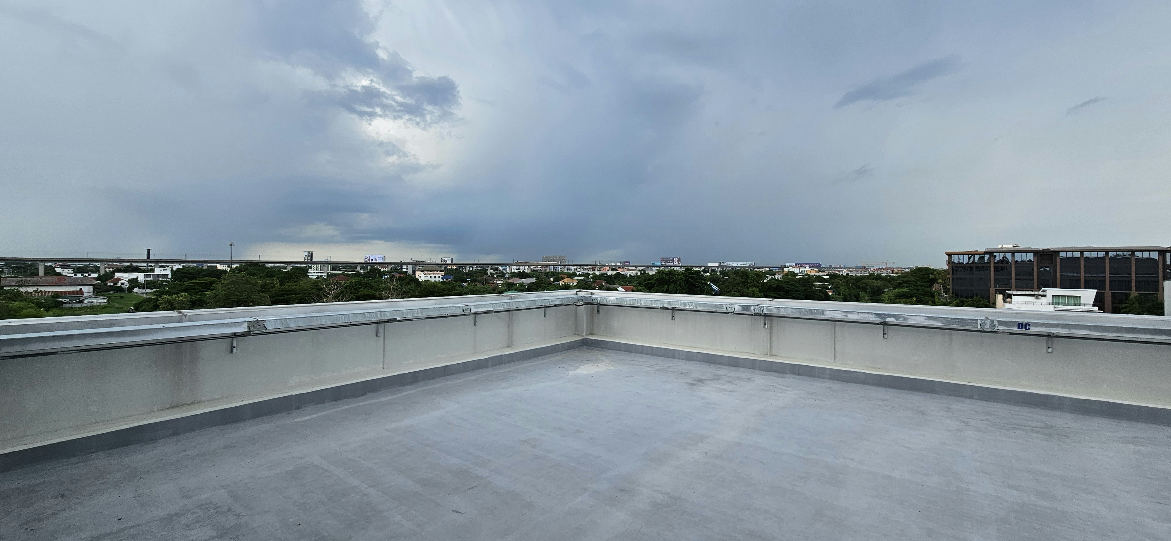 Rooftop terrace with a low concrete parapet overlooks a distant city under a dramatic stormy sky.
