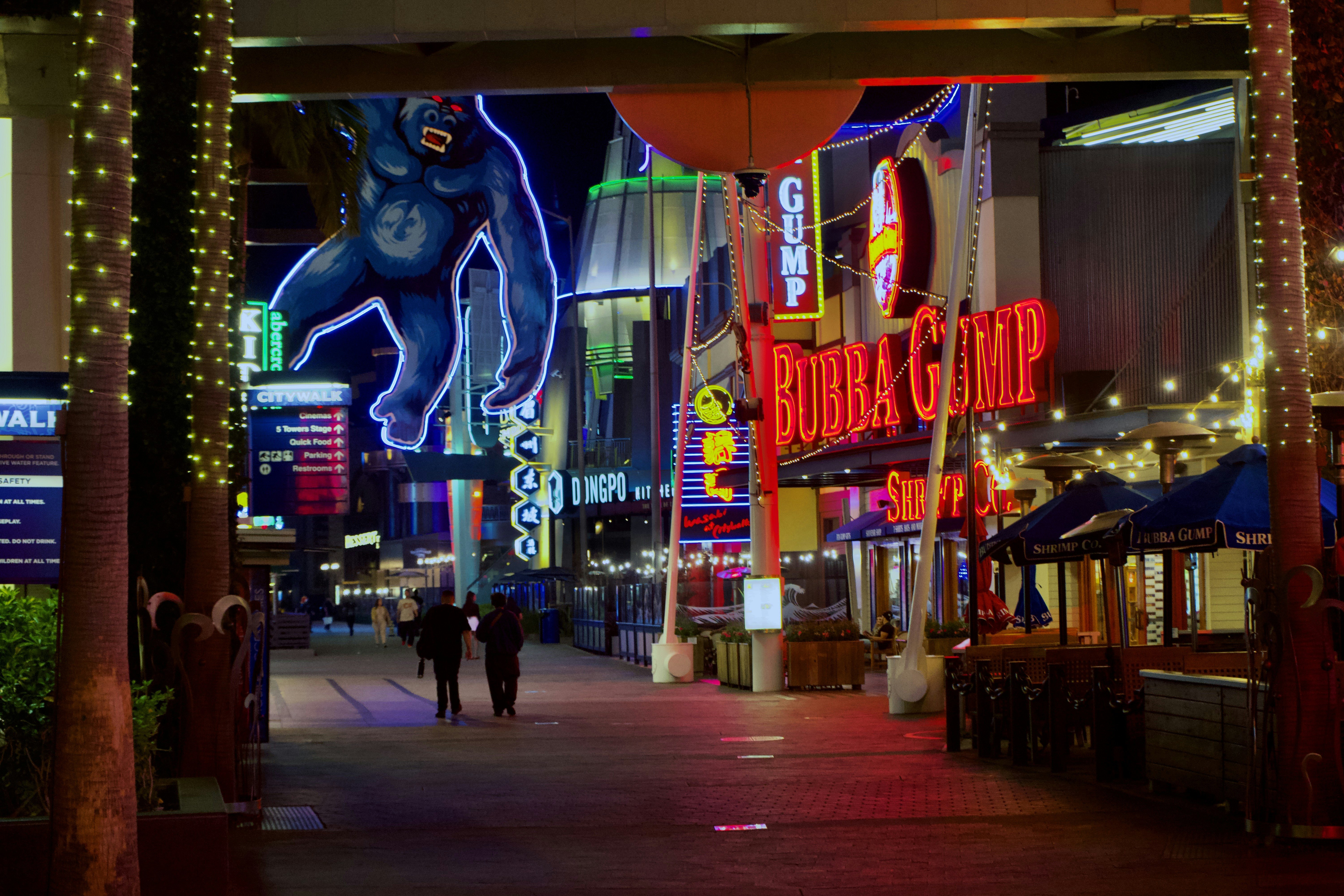 Vibrant city street illuminated by colorful neon signs and lively storefronts at night.