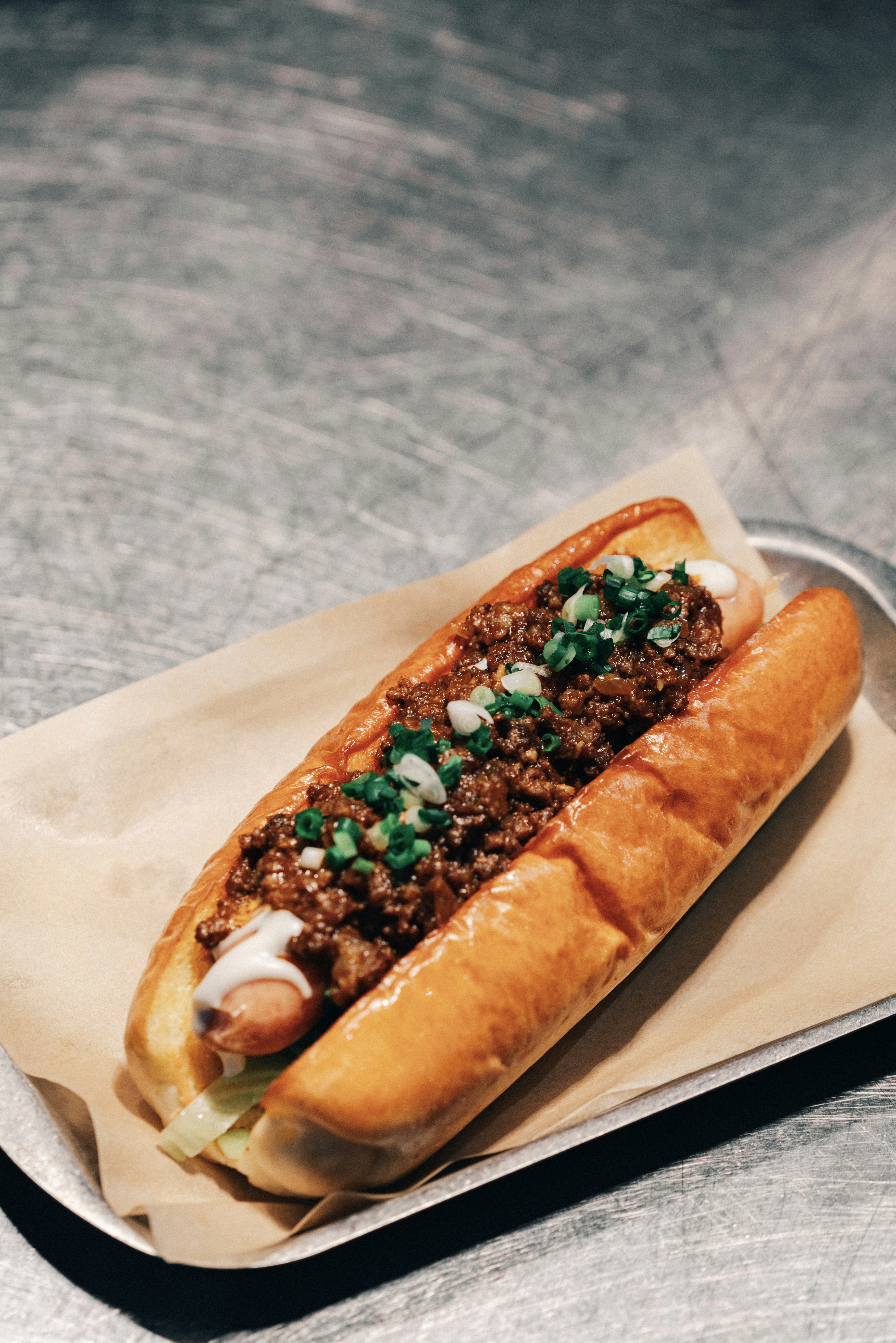 Gourmet hot dog topped with seasoned meat and fresh green onions, resting on a parchment-lined tray.