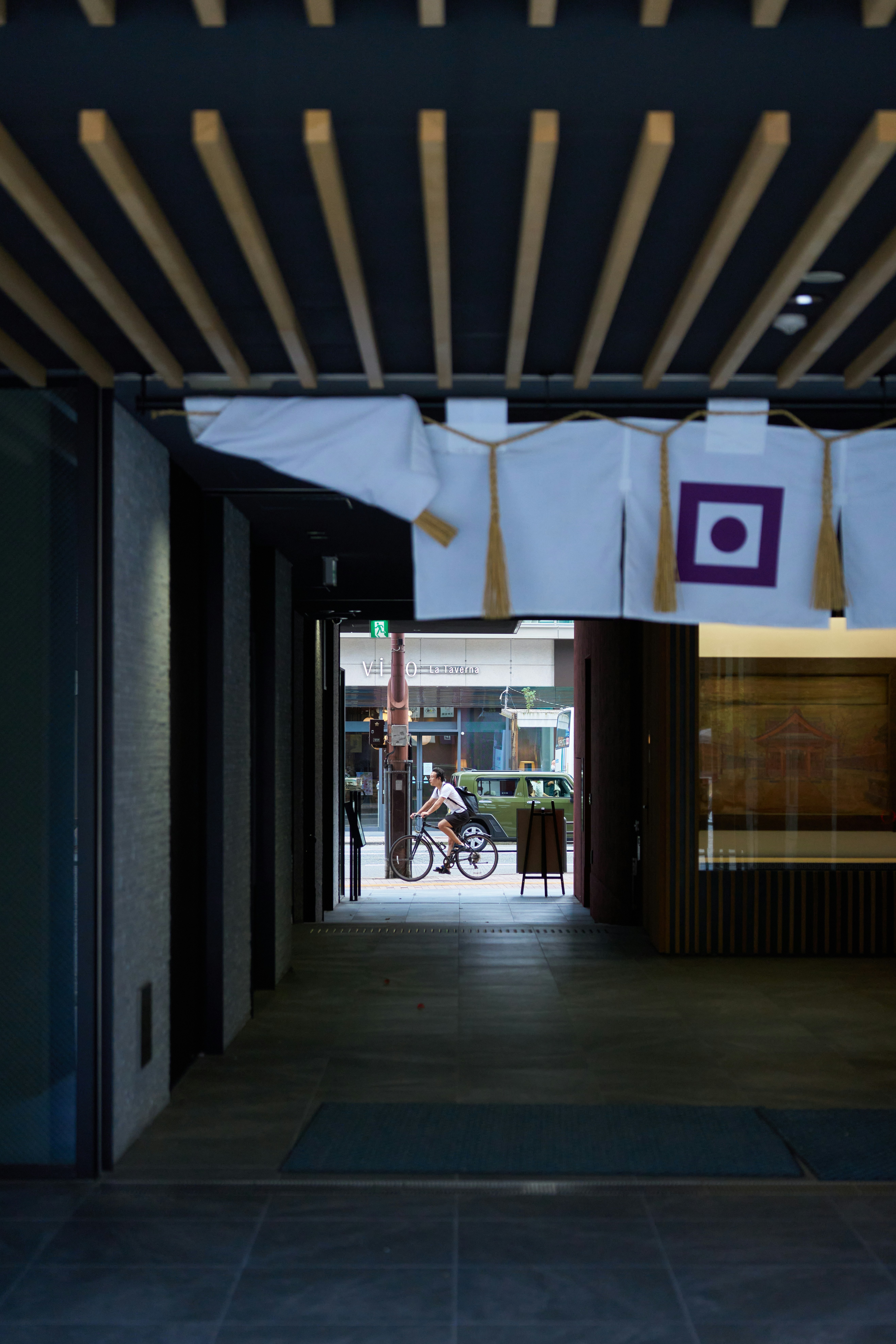 Through the Corridor: A Cyclist Emerges Under a White Banner