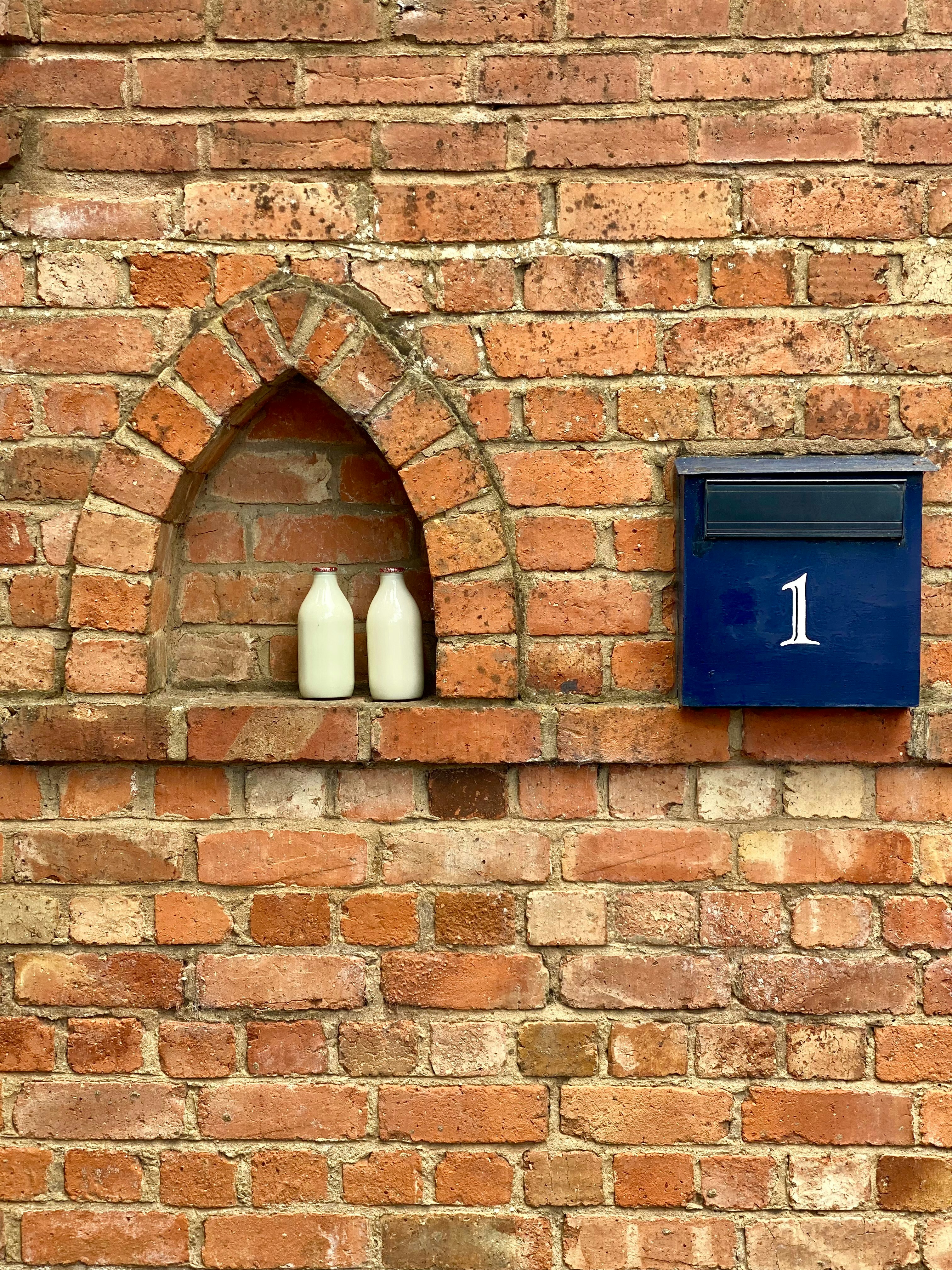 Niche of Cream: Two Milk Bottles in a Brick Arch Next to a Blue Mailbox
