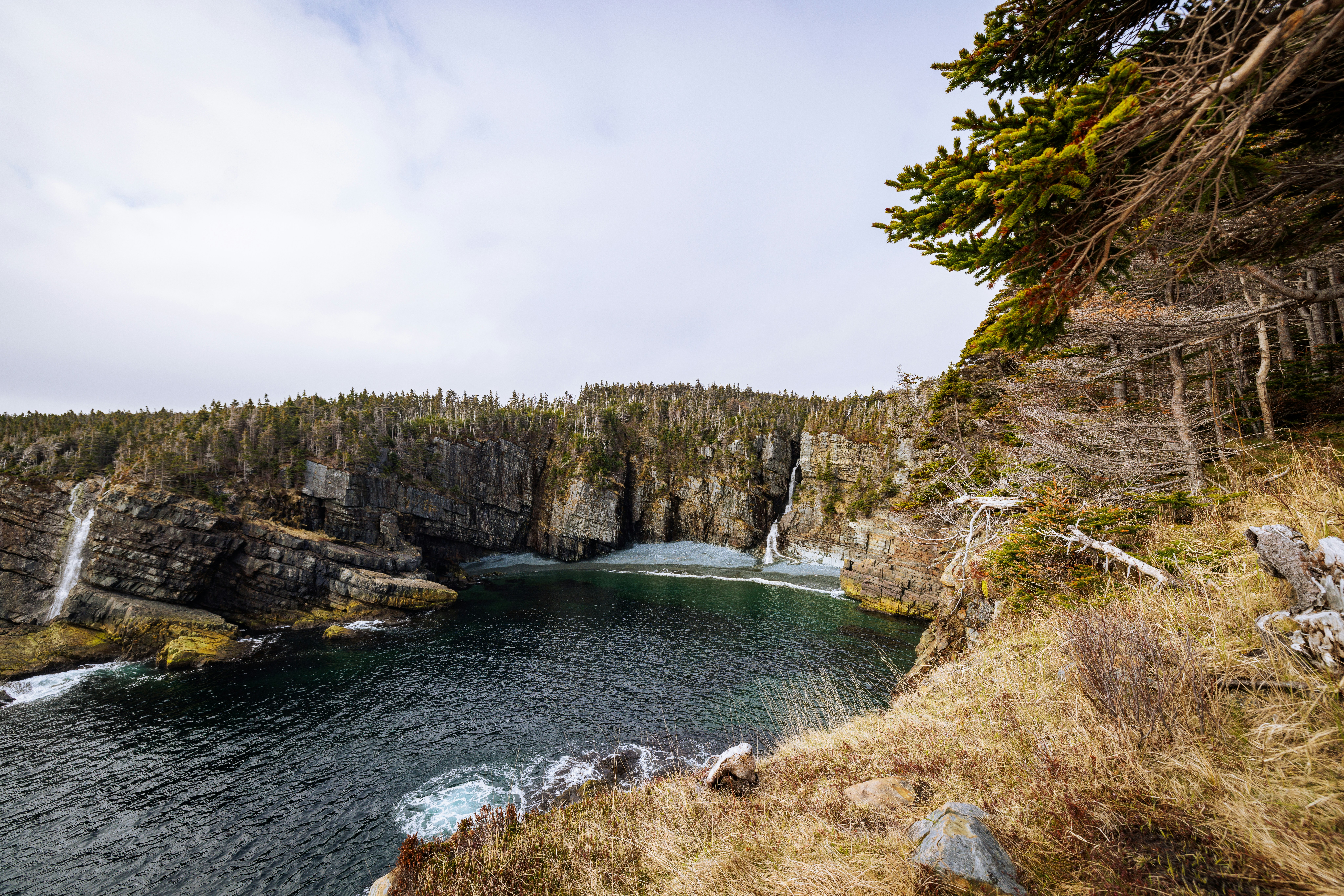 A serene landscape featuring a tranquil cove surrounded by rugged cliffs and gentle waterfalls, framed by lush greenery and rocky terrain.