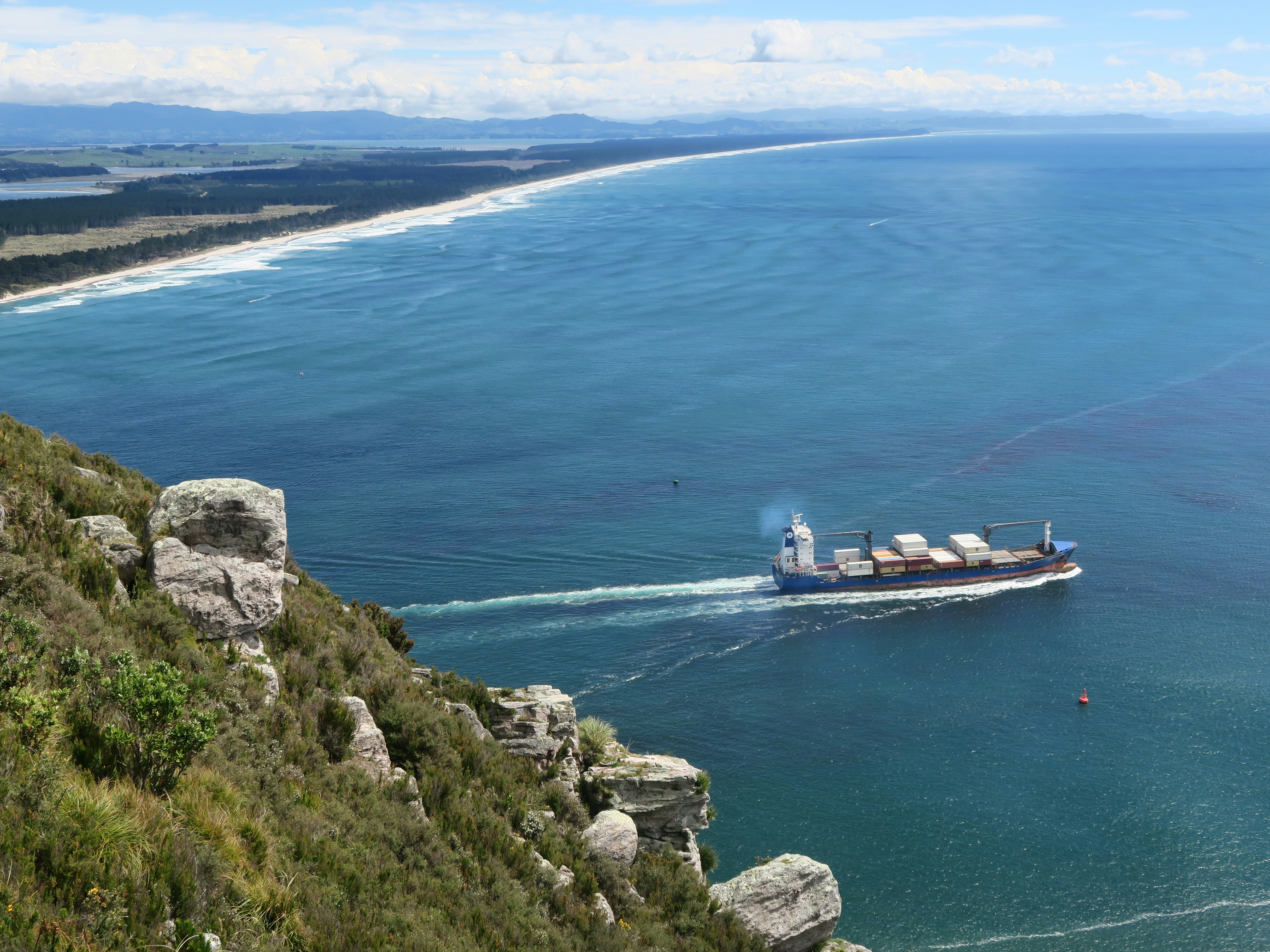 Cargo ship navigating the expansive blue sea alongside a rugged cliff.