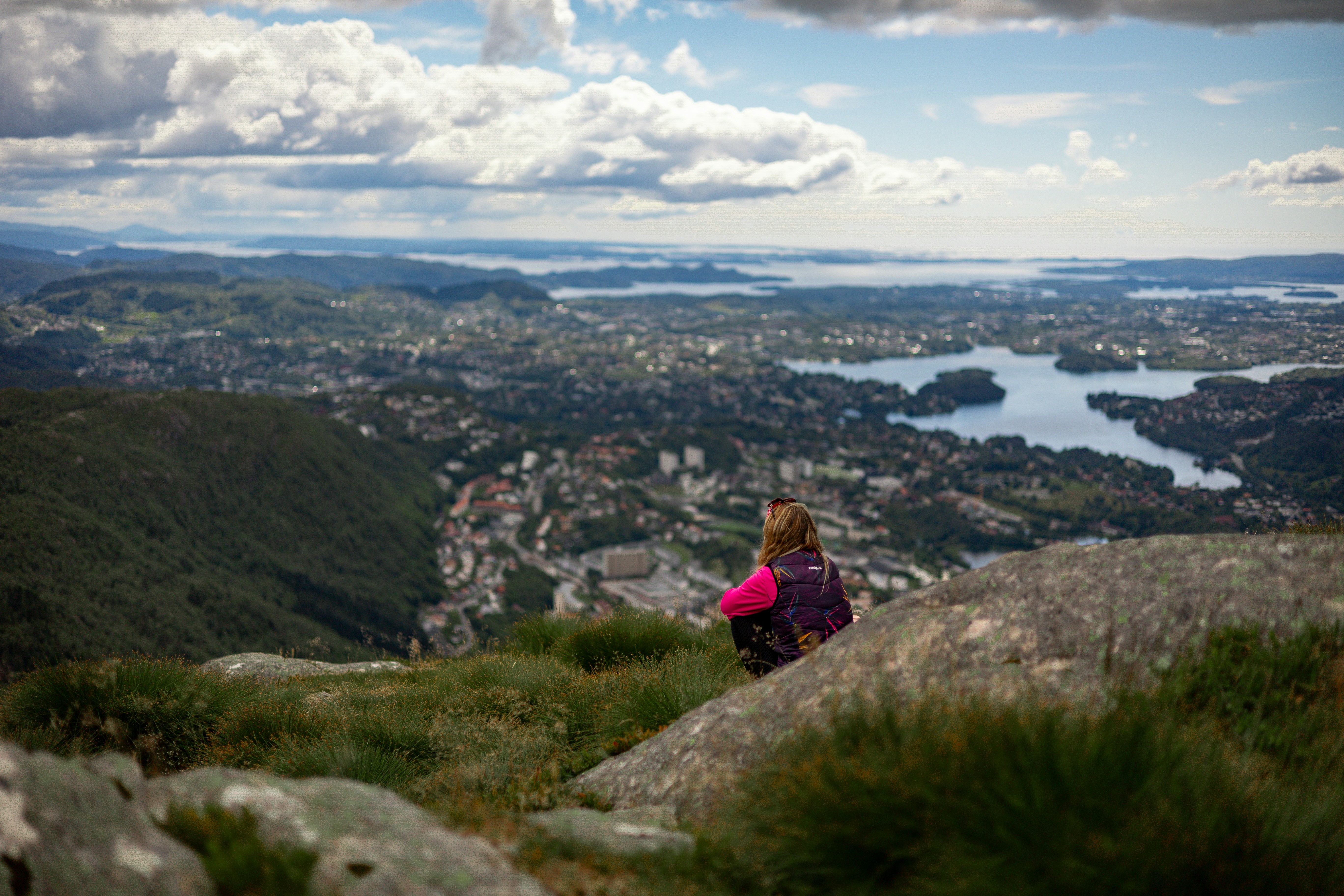A woman sitting on top of a hill overlooking a city photo – Free ...