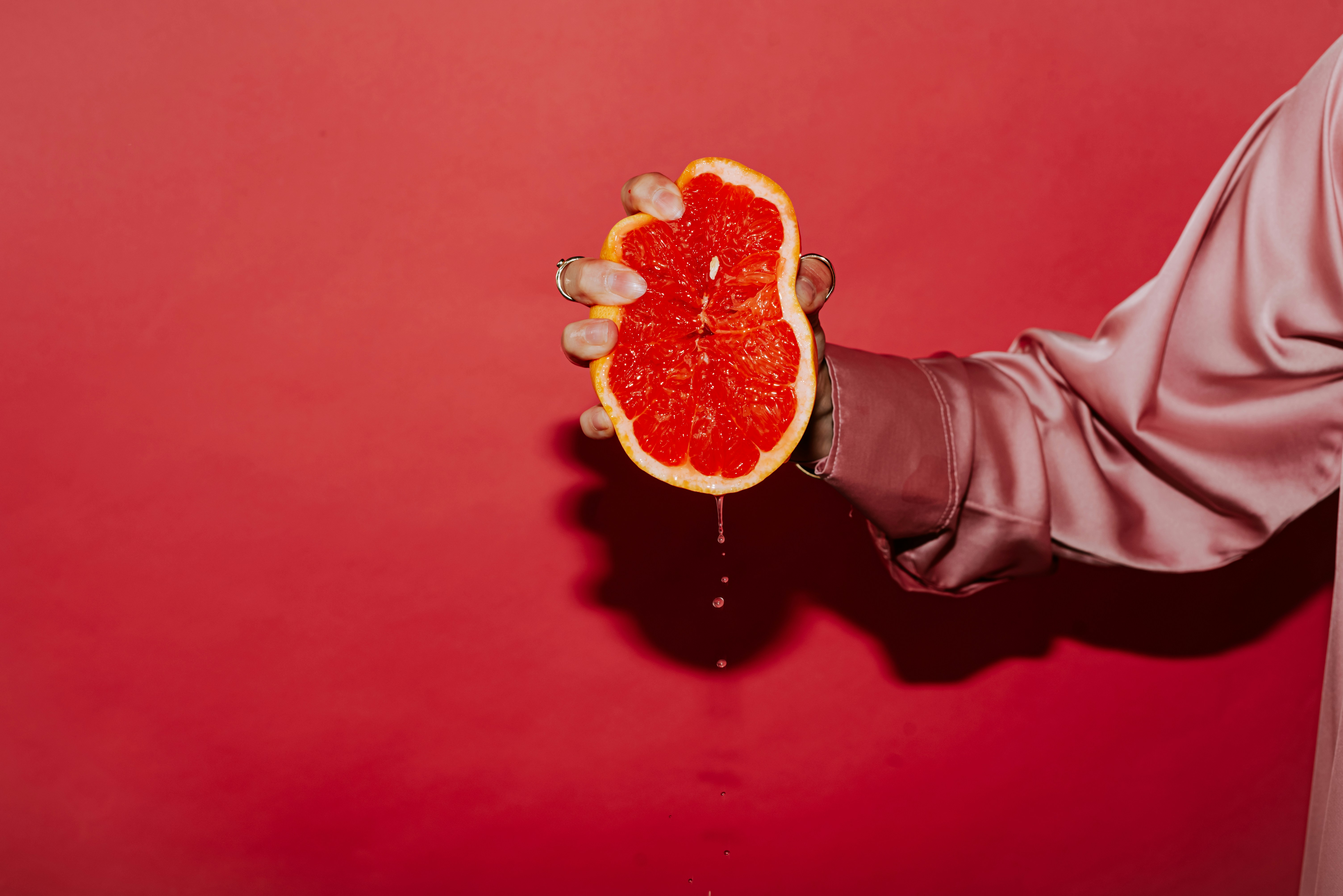Crimson Citrus Portrait: Hand-Held Grapefruit Against Velvet Red