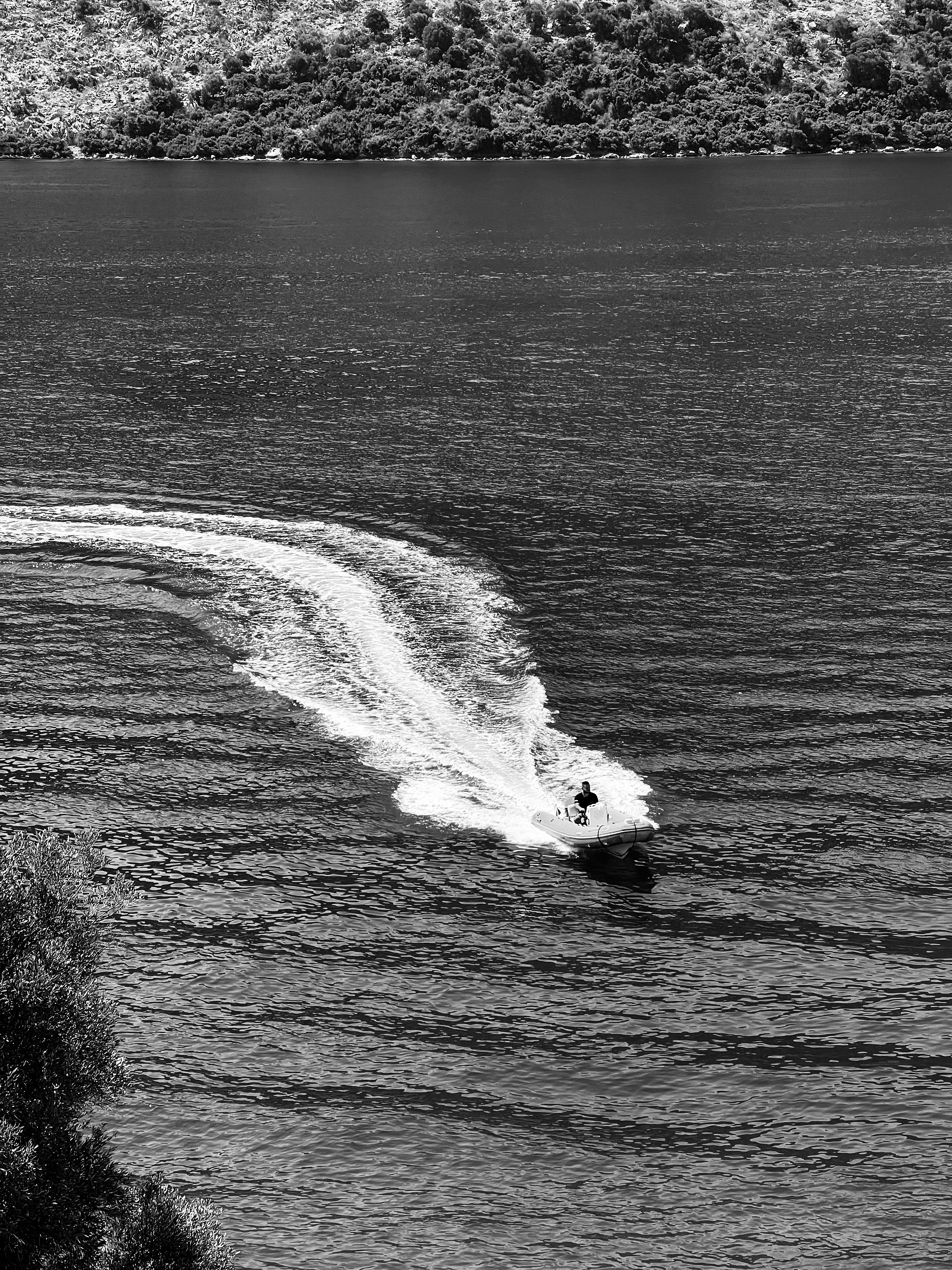 Monochrome Arc: A lone speedboat carves a curved wake across a lake