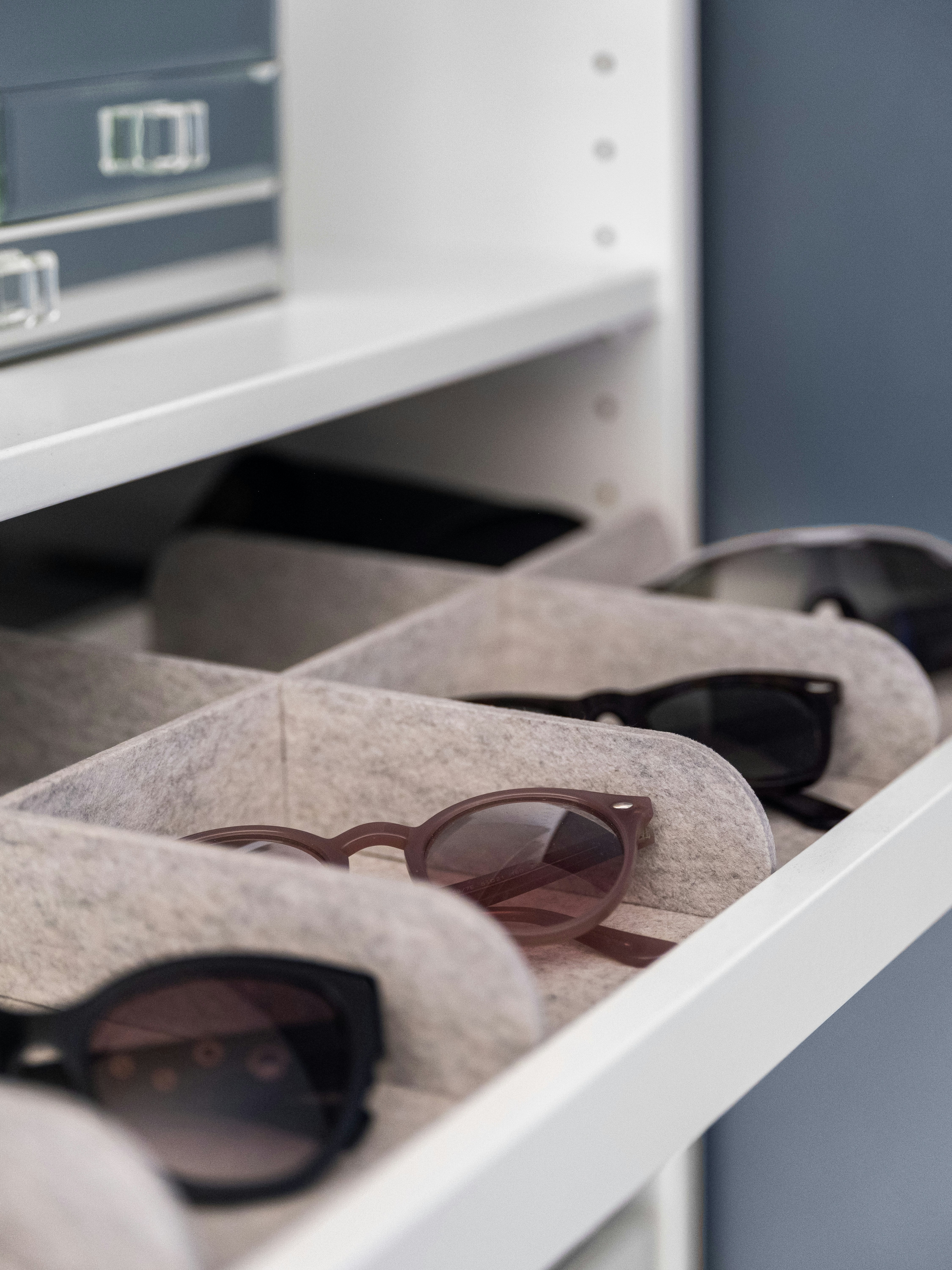 Sunglasses neatly arranged in a felt-lined drawer organizer inside a cabinet, with a shallow depth of field.