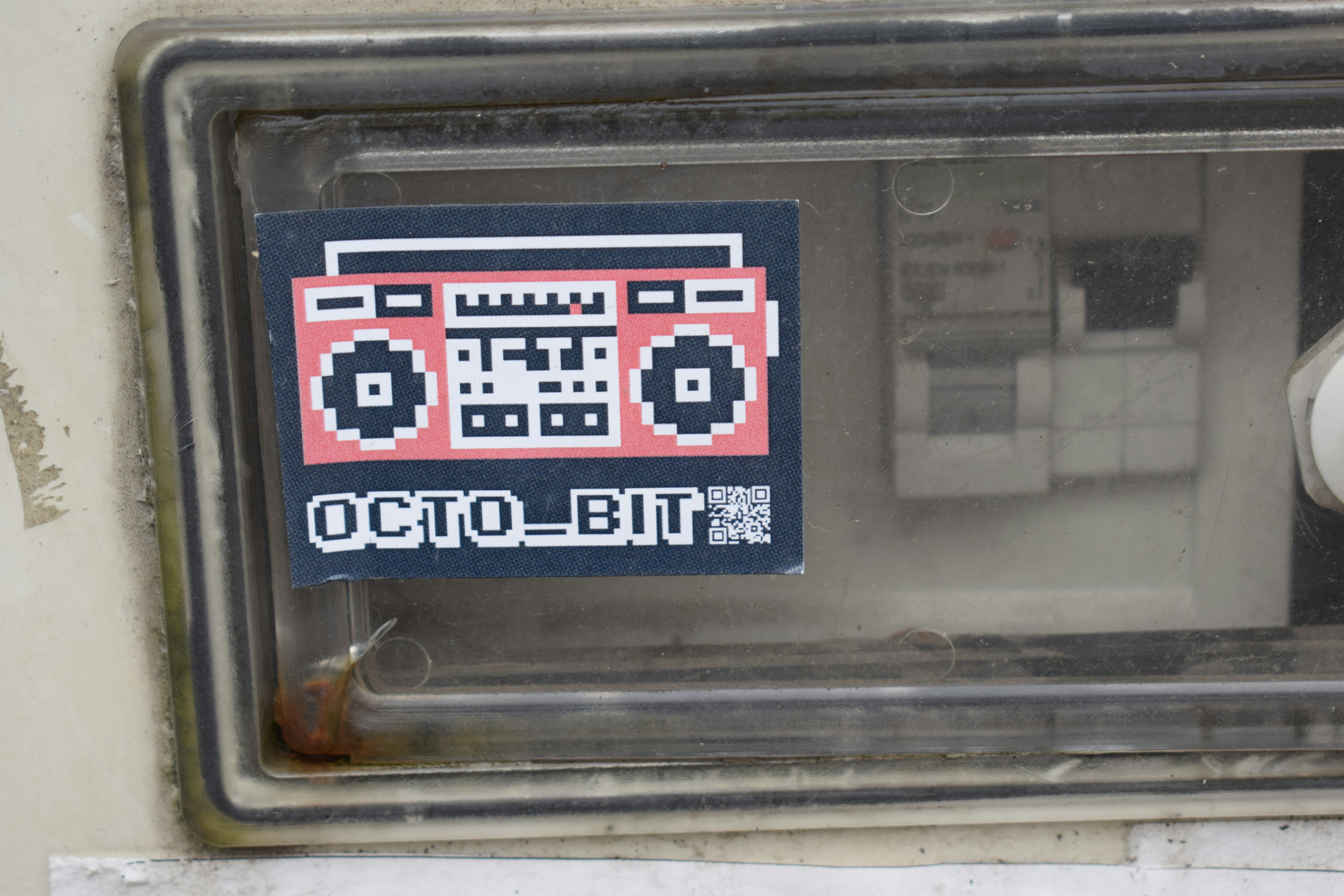 Octo_Bit Sticker on a Weathered Mailbox Glass