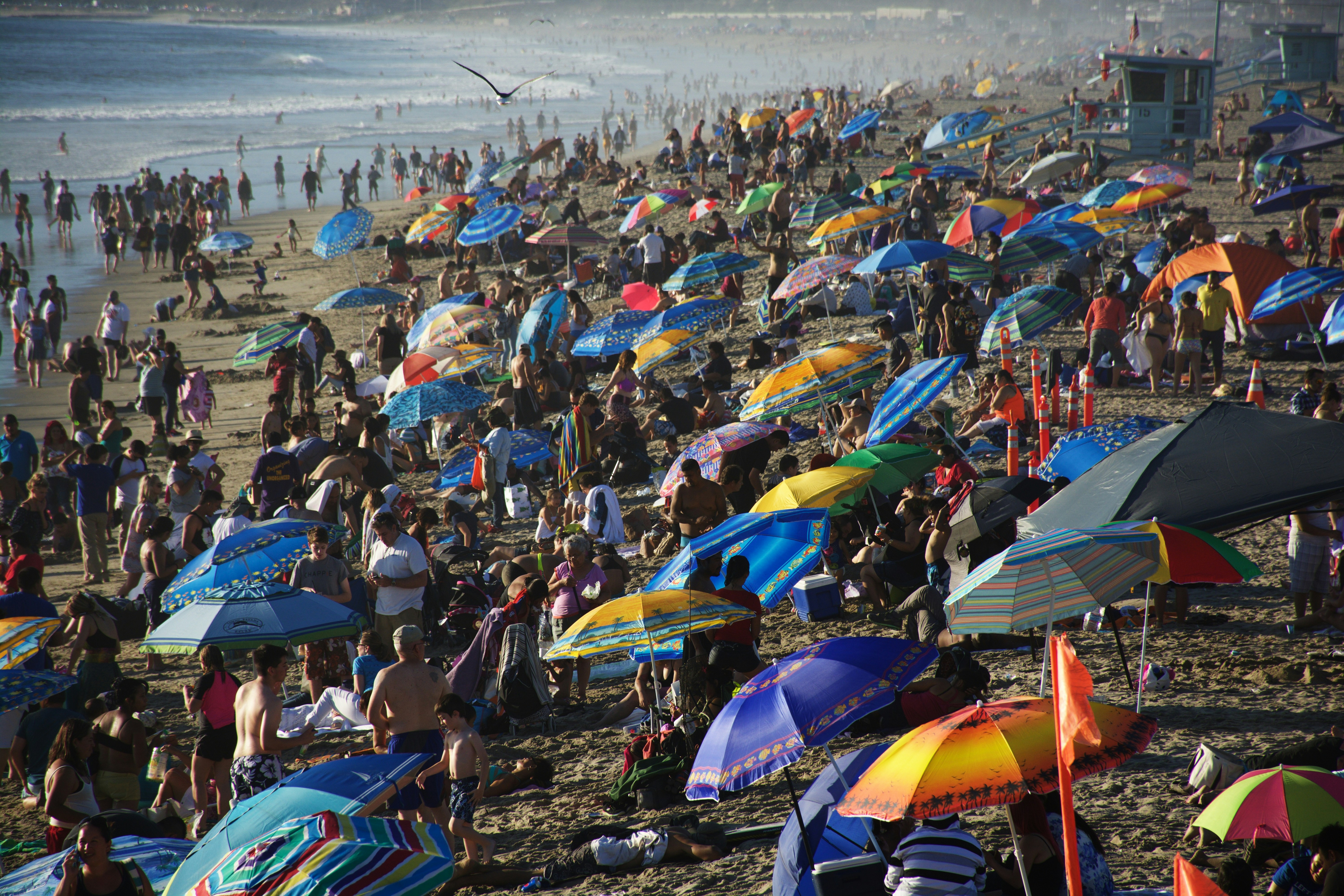 Crowded beach scene filled with colorful umbrellas, sunbathers, and waves, capturing the essence of summer leisure.