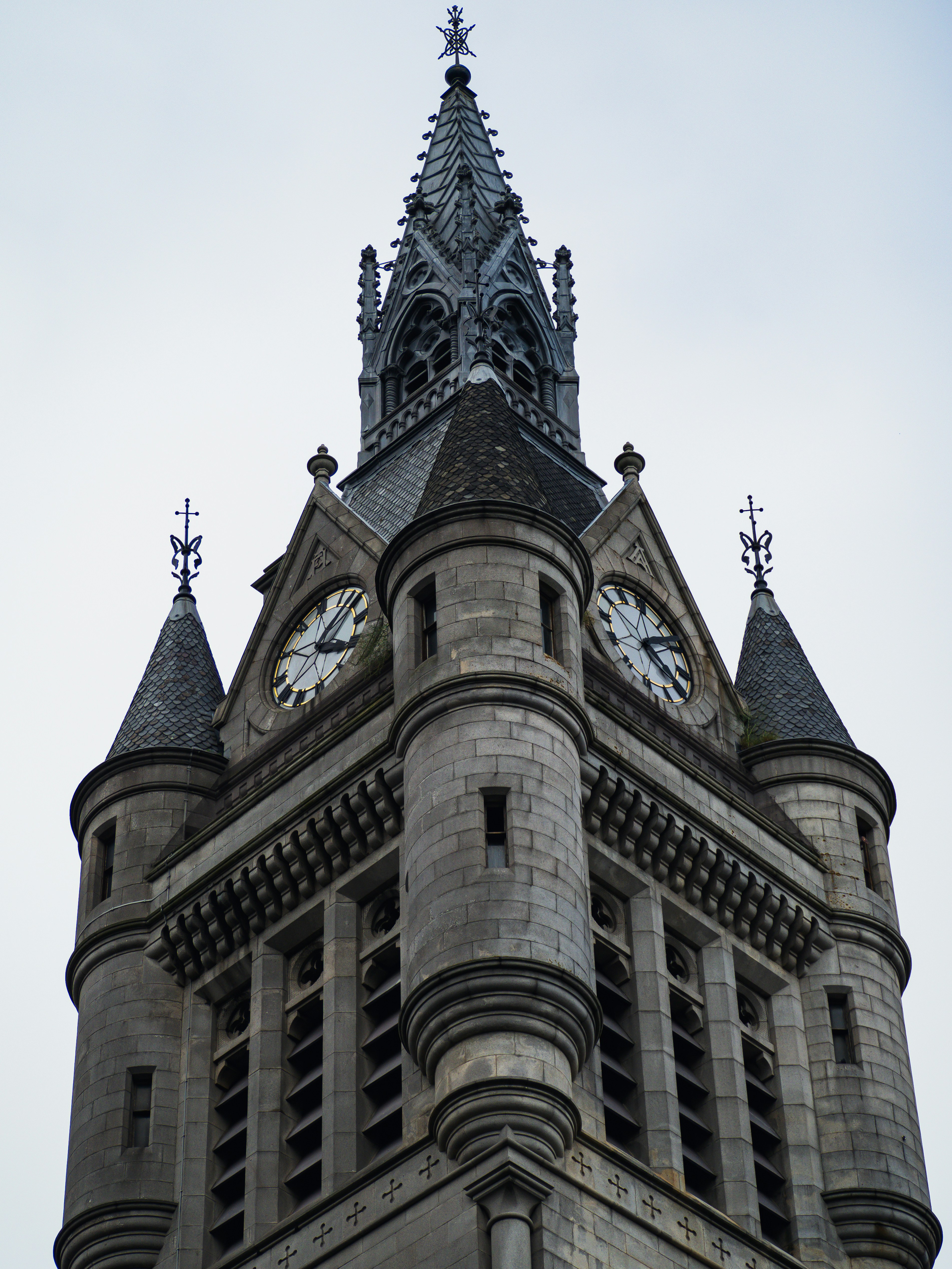 Stone clock tower with intricate Gothic details against a cloudy sky.