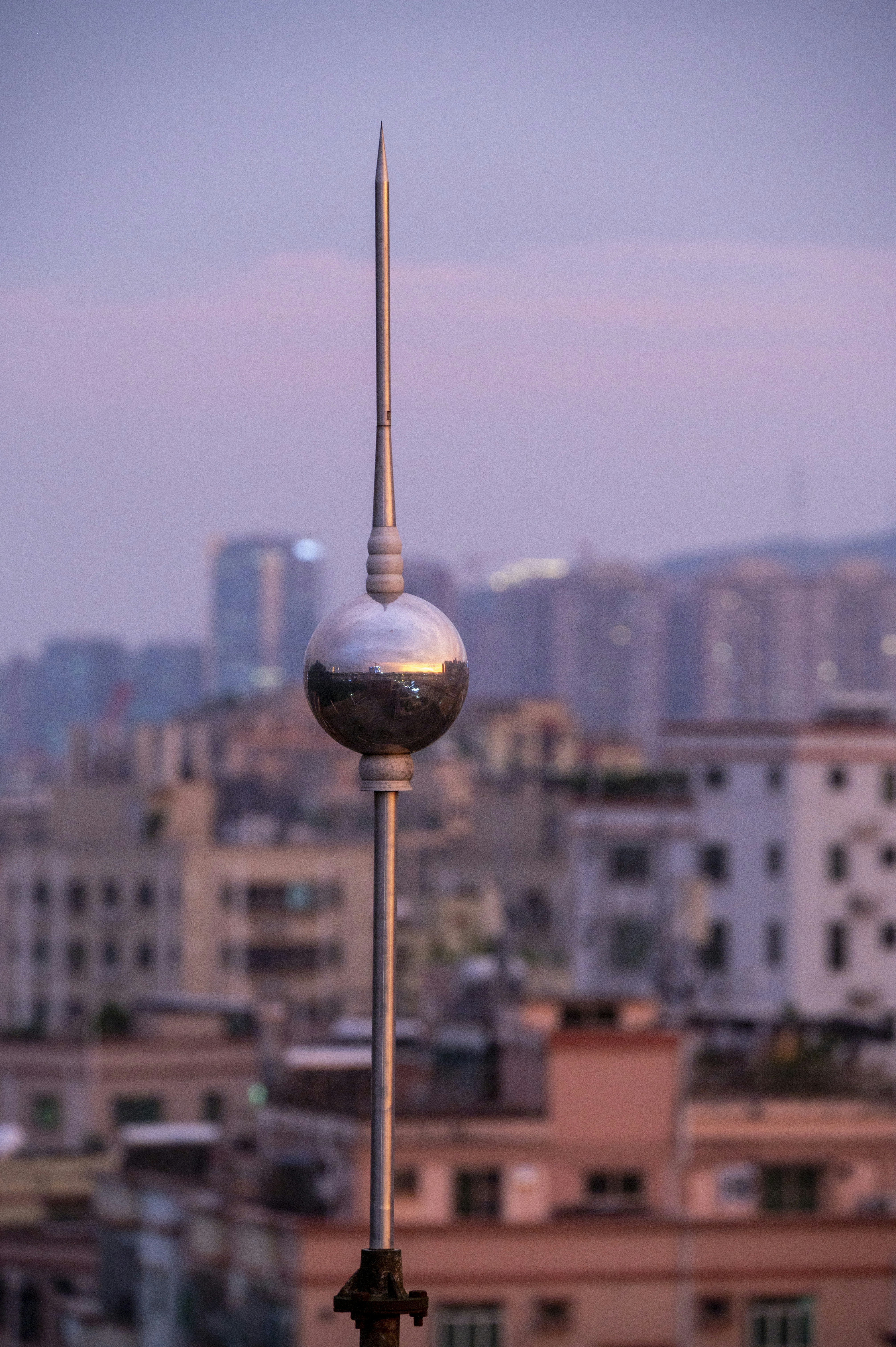 Dusk Spire: A polished orb crowns a rooftop antenna over a softened cityscape.