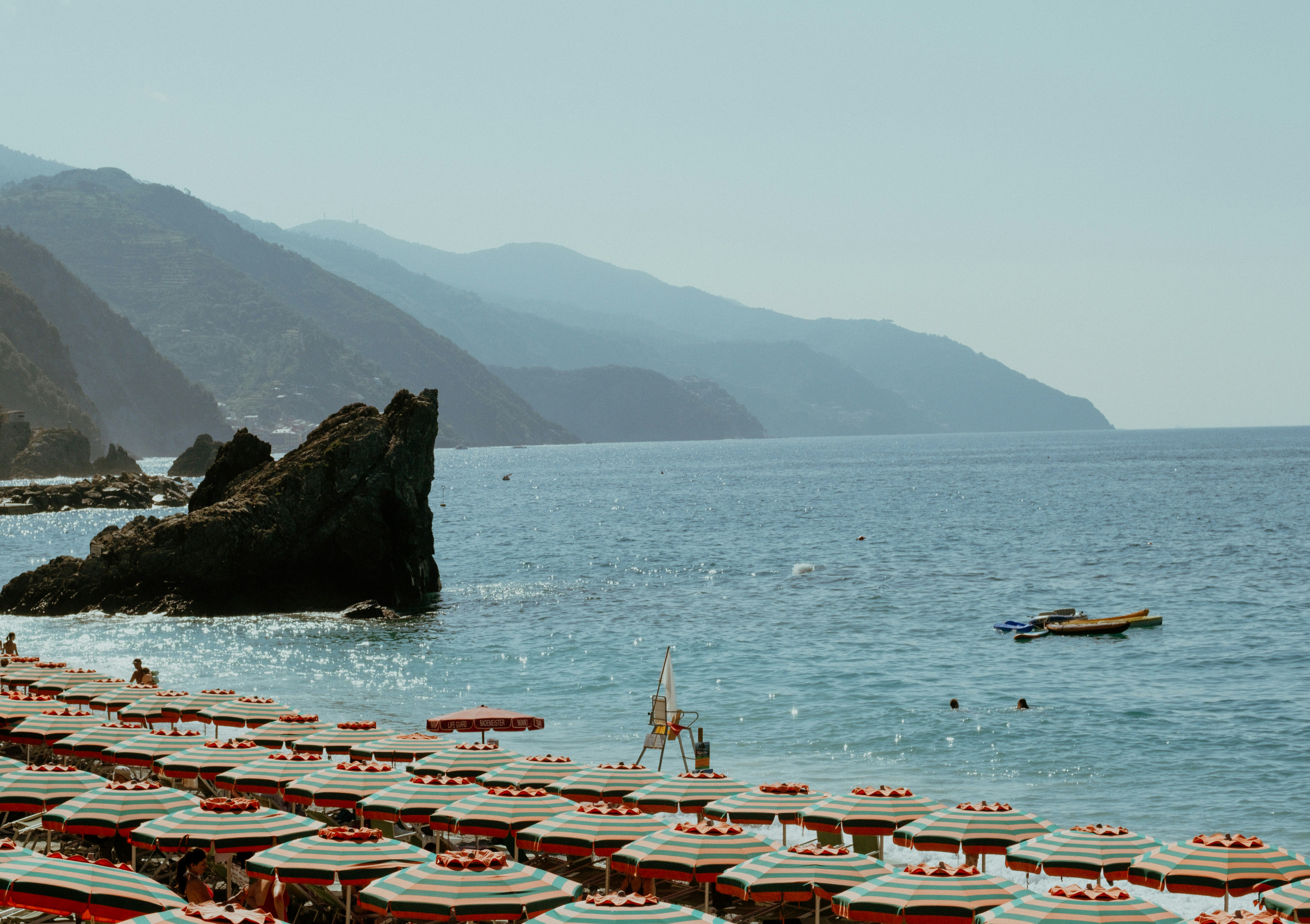 Rows of beach umbrellas line the shore with mountains and sea in the background.