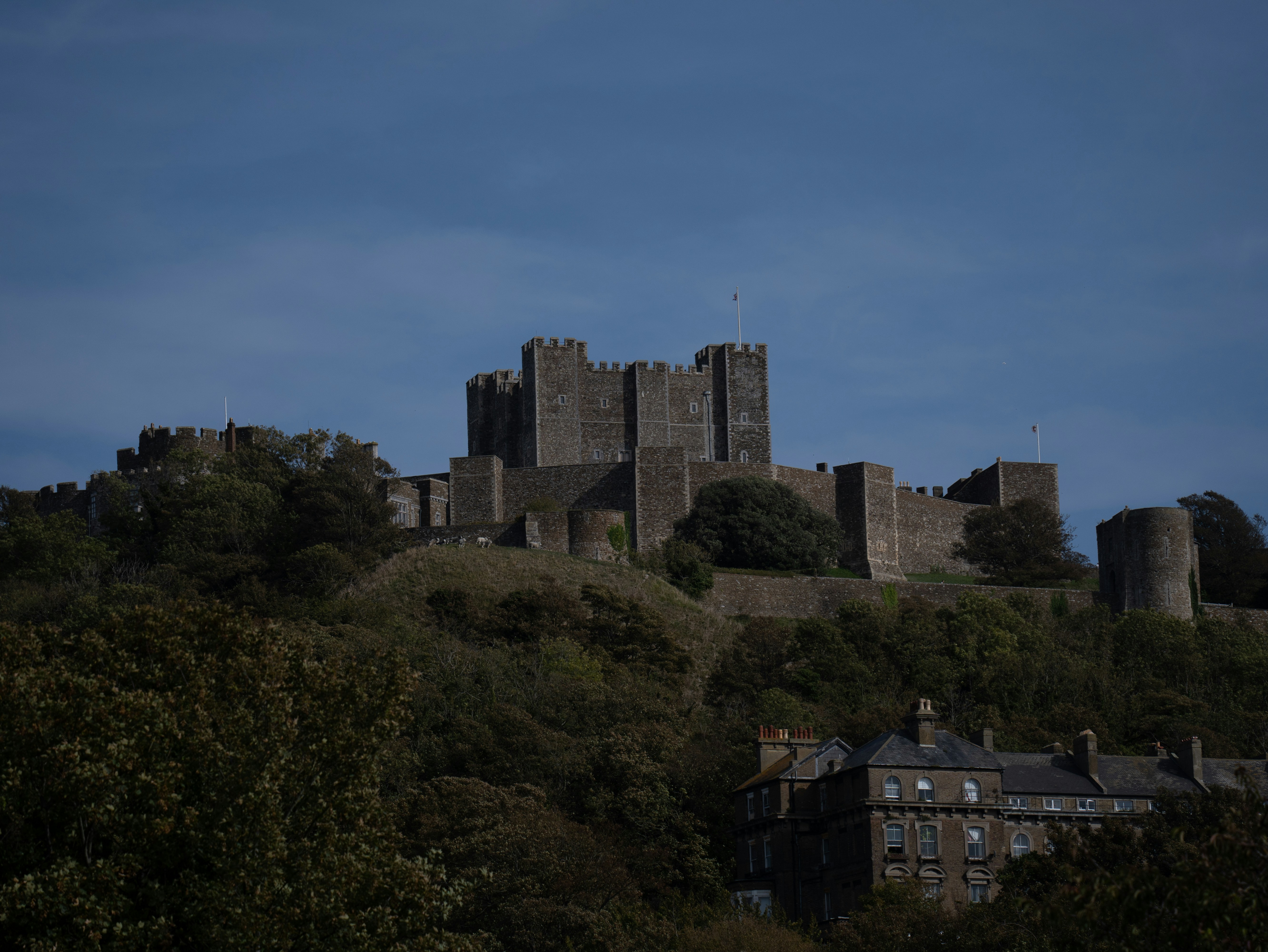 Historic stone castle perched atop a hill surrounded by lush greenery under a deep blue sky.