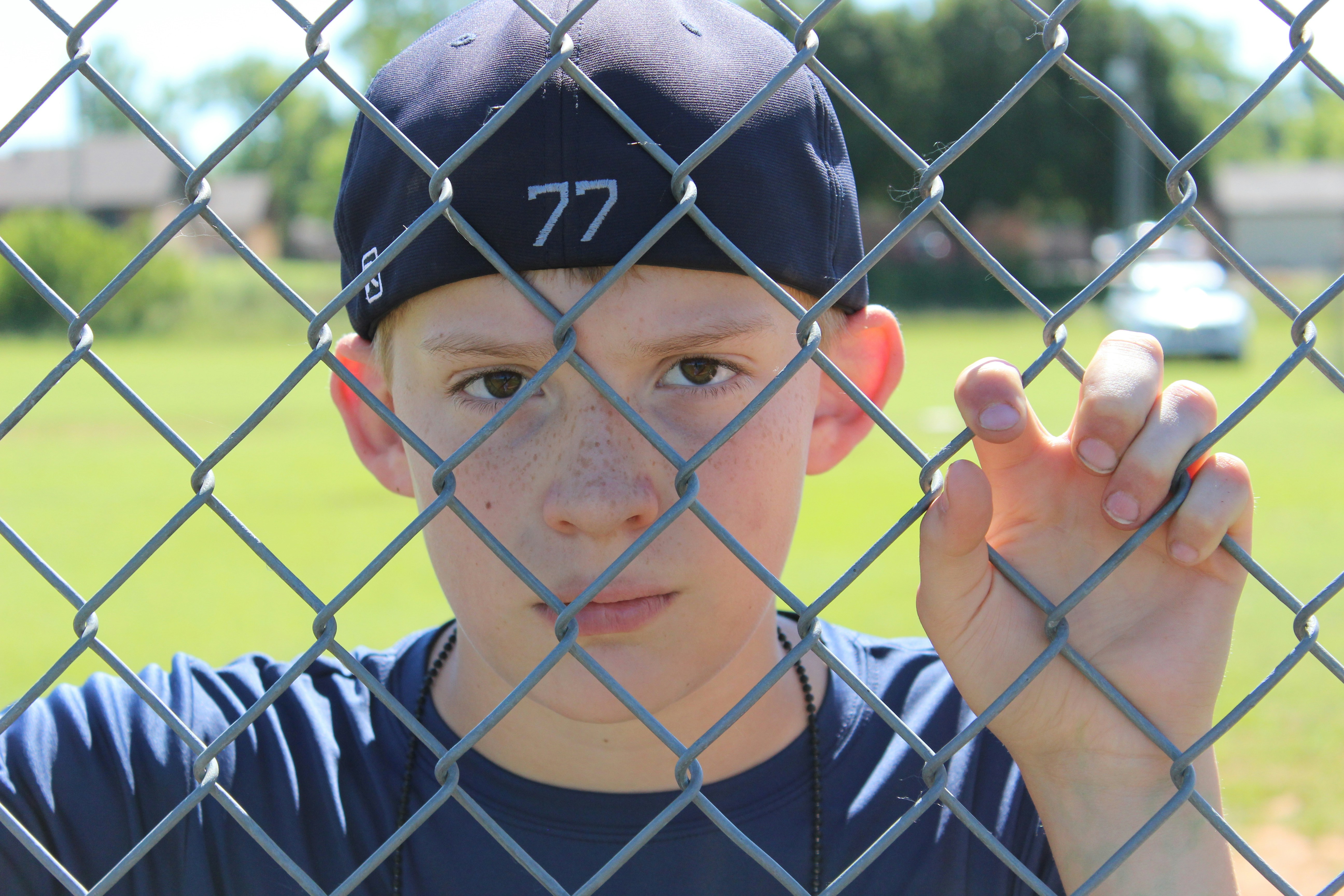 A young boy holding a baseball bat behind a fence photo – Free Portrait ...